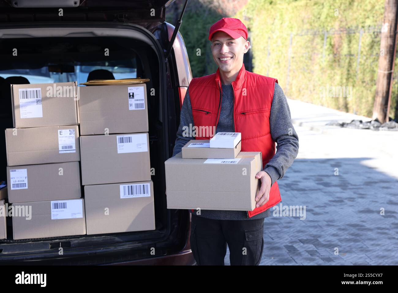 Happy postman with parcels near car outdoors Stock Photo - Alamy