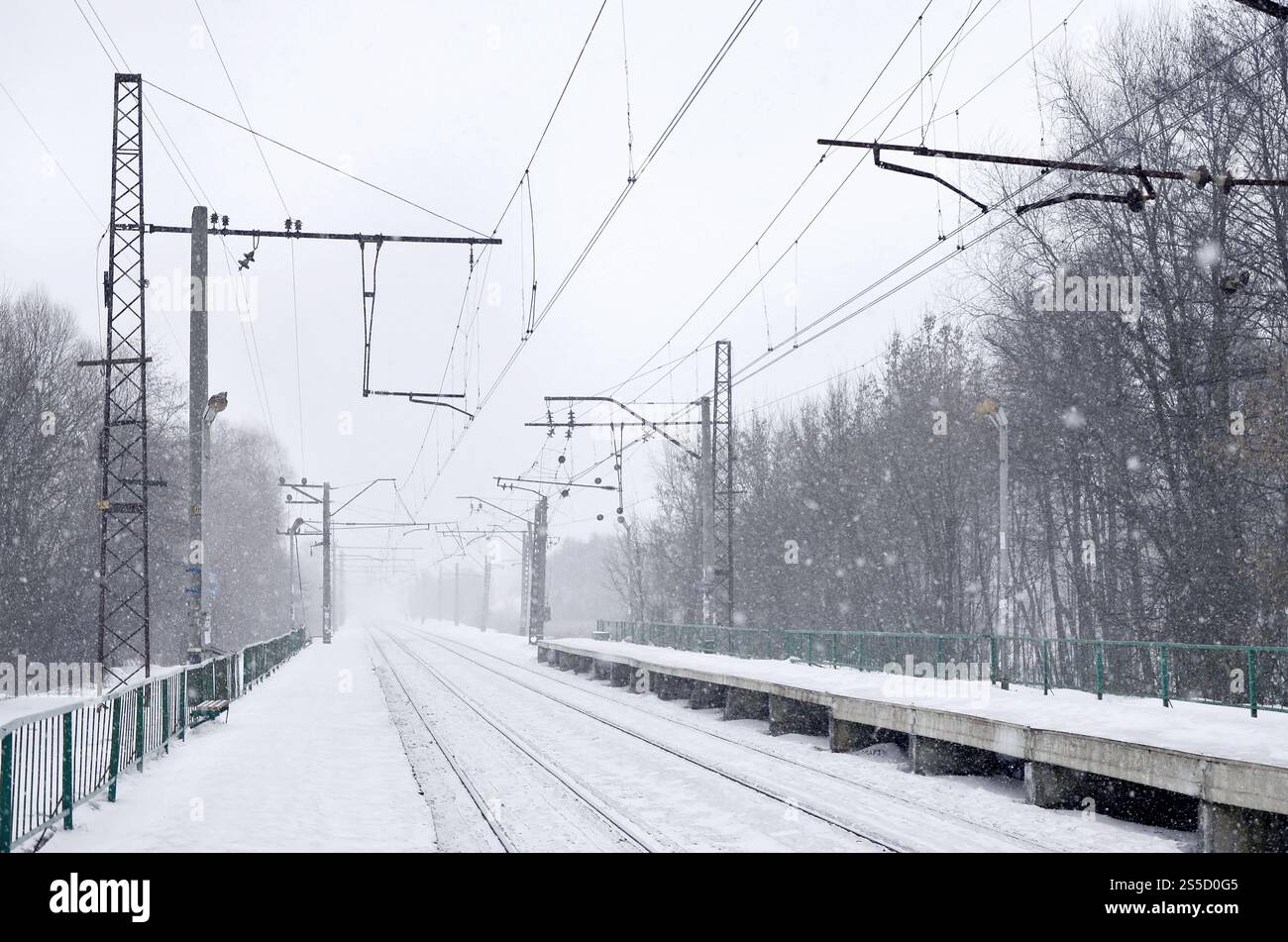 Empty railway station in heavy snowfall with thick fog. Railway rails ...