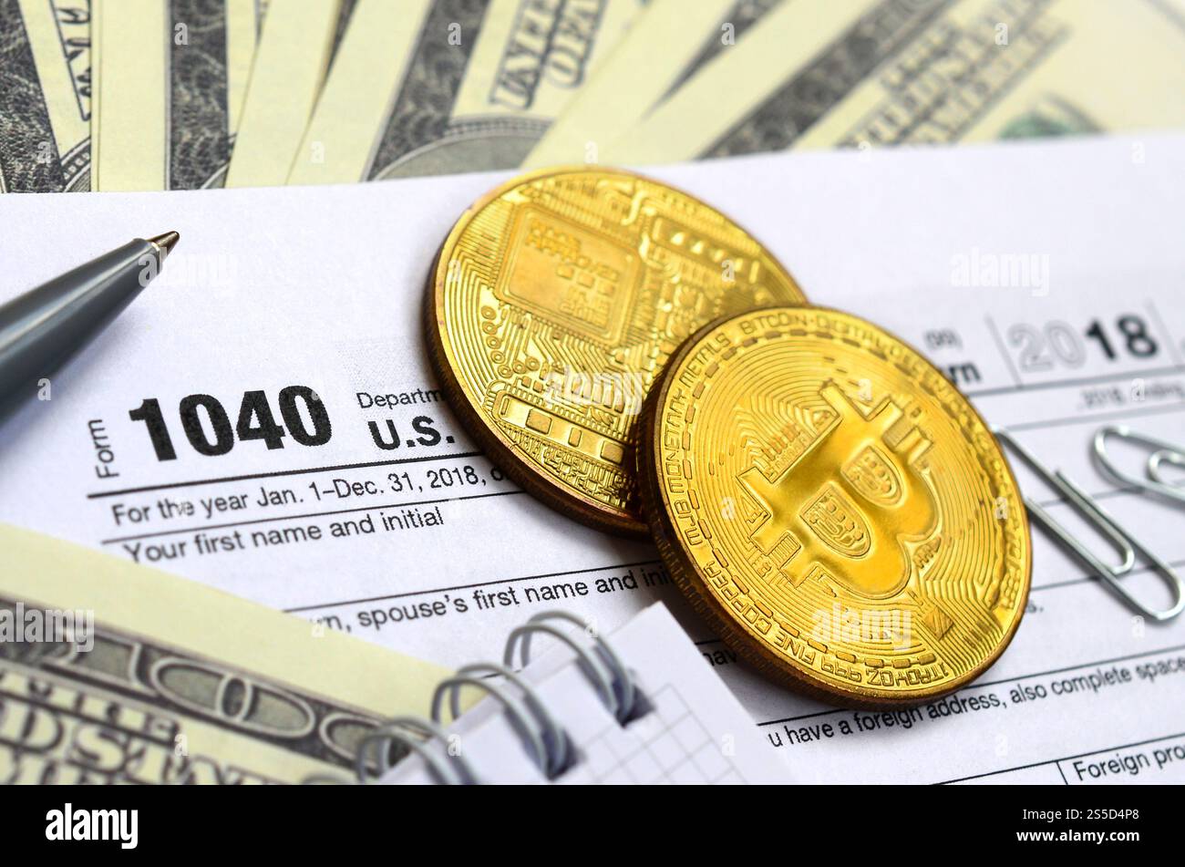 The pen, bitcoins and dollar bills is lies on the tax form 1040 U.S ...