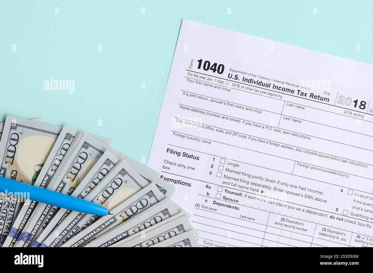 1040 tax form lies near hundred dollar bills and blue pen on a light ...