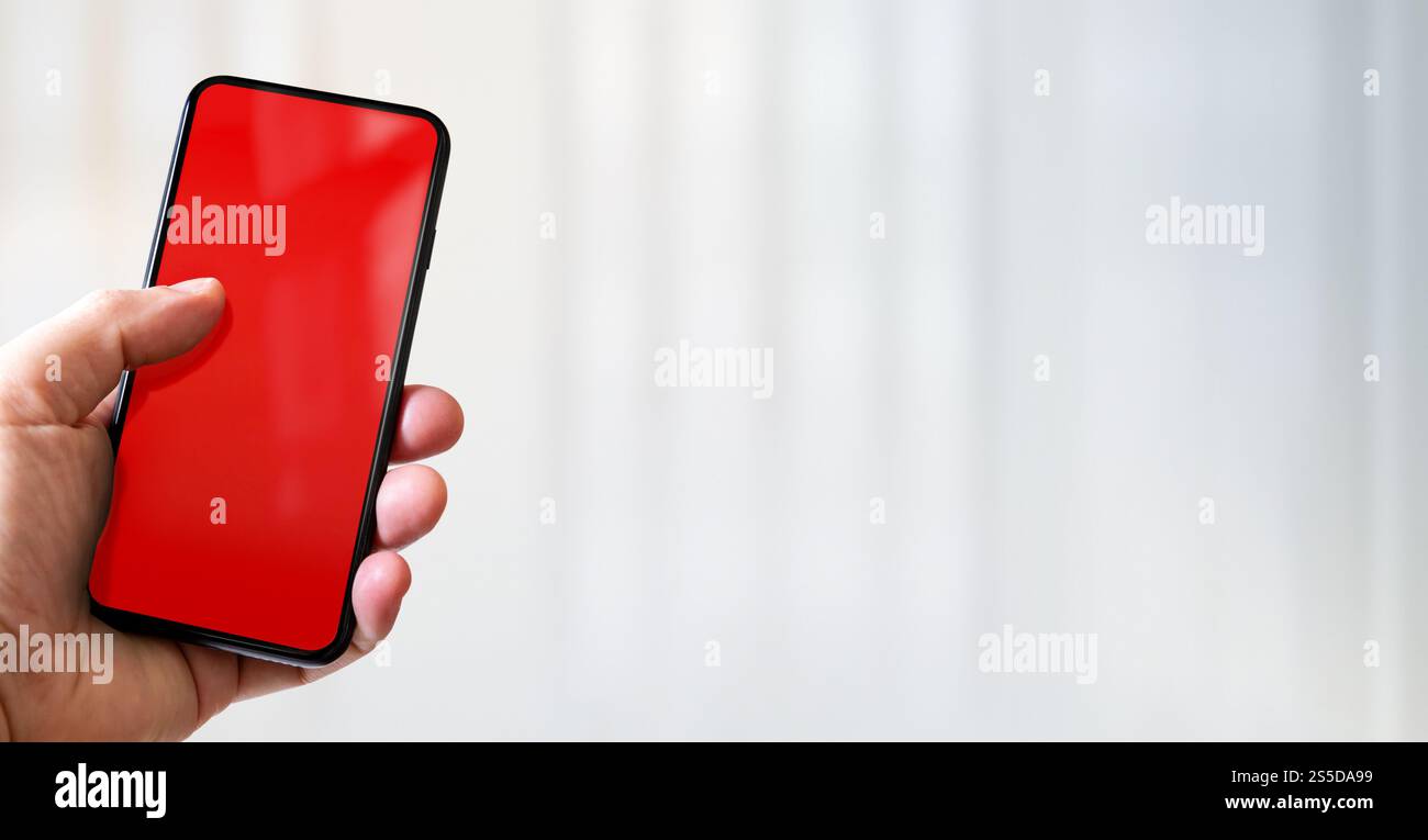 Hand holding a smartphone with blank red screen. White office ...