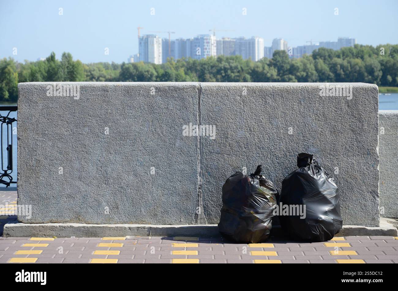 Two black garbage bags on tiled street floor at concrete fence in city ...