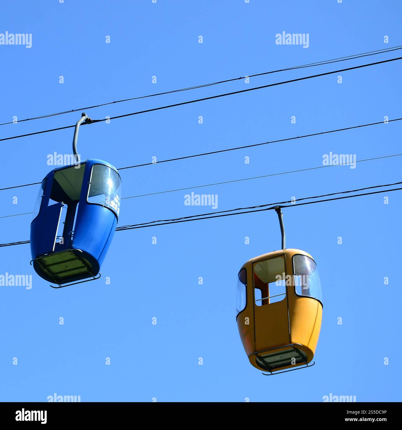 Blue and yellow passenger cable way cabins in the clear blue sky. Blue ...