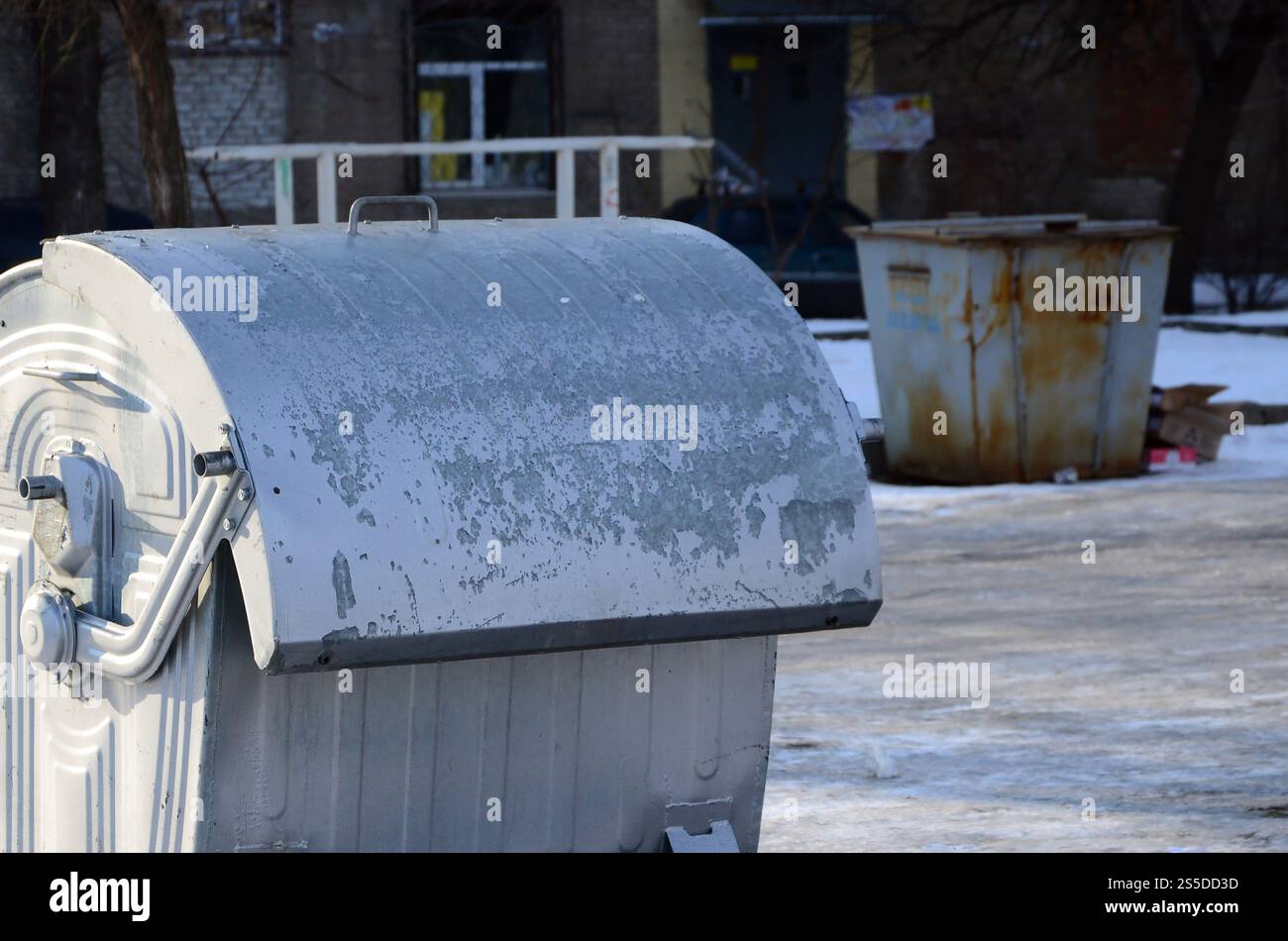 A silver garbage container stands near residential buildings in winter ...