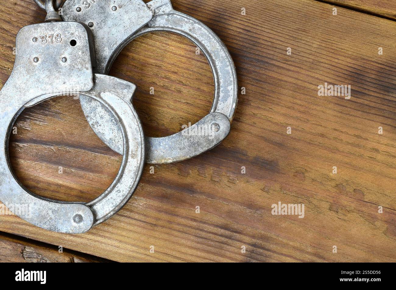 Old and rusty police handcuffs lie on a scratched wooden surface. The ...