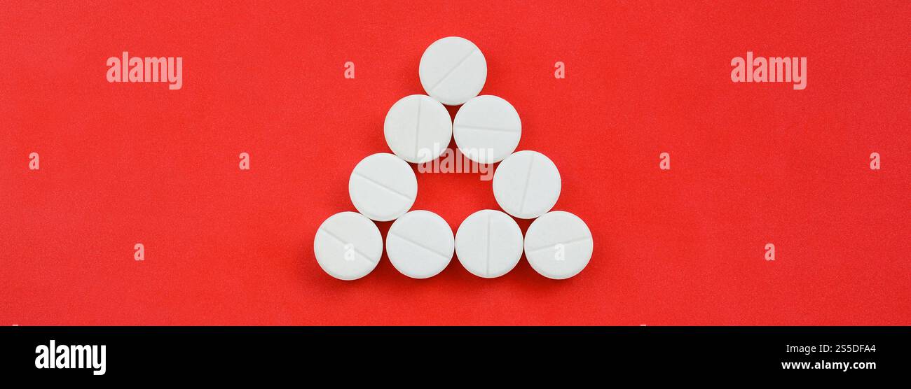 Several white tablets lie on a bright red background in the form of an ...