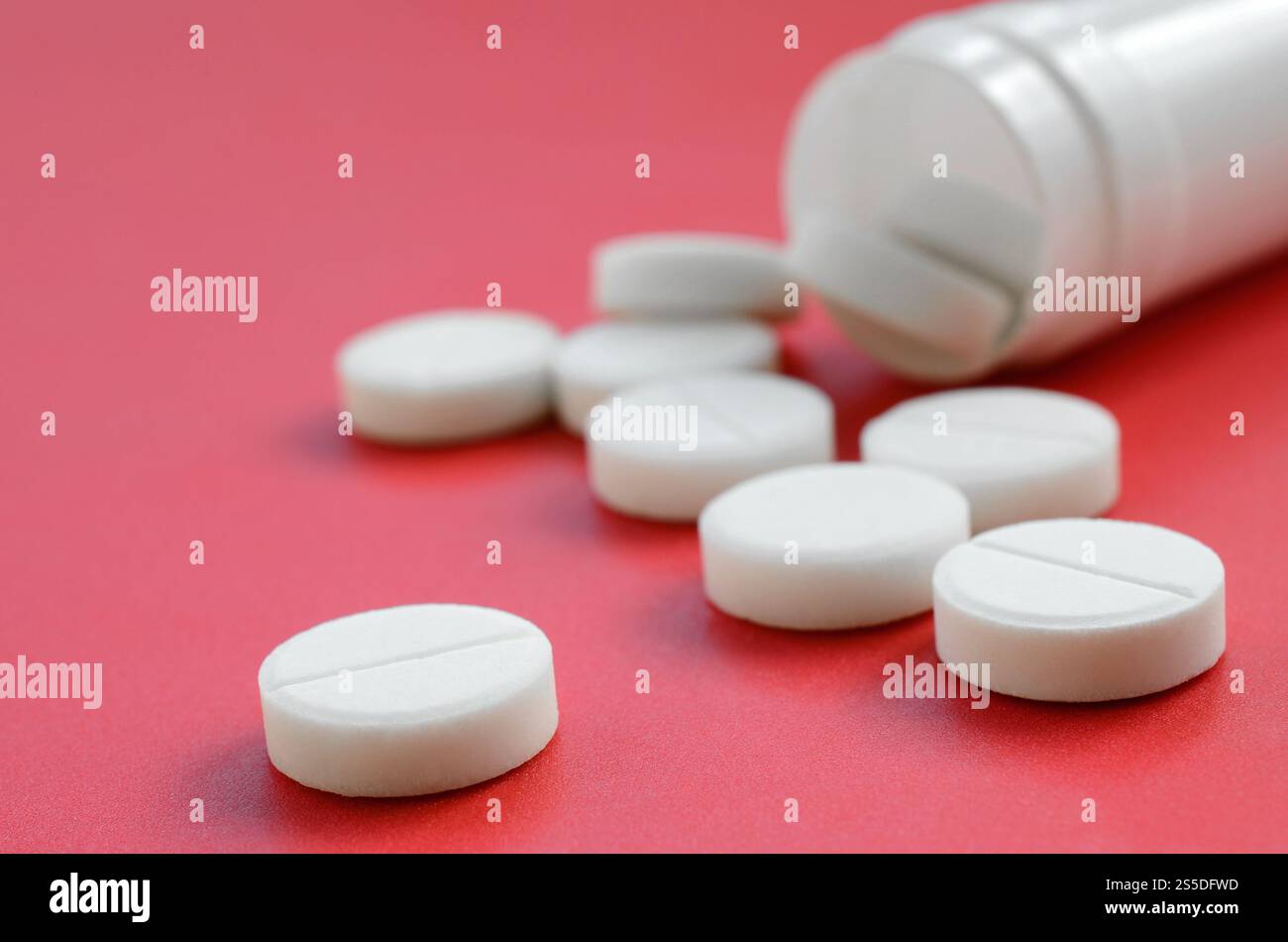 Several white tablets fall out of the plastic jar on the red surface ...