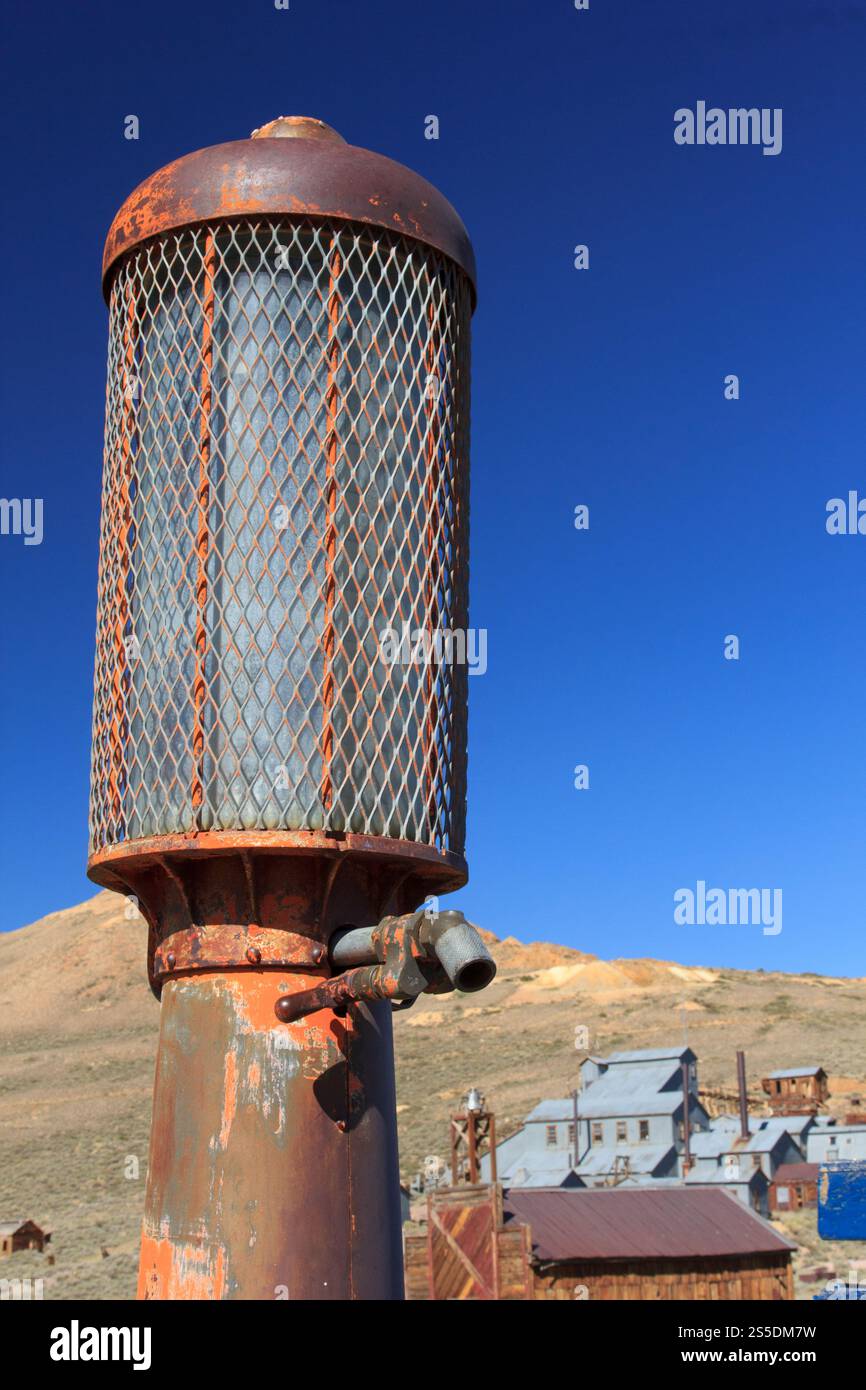 A rusty metal light fixture is sitting on a pole in front of a blue sky ...