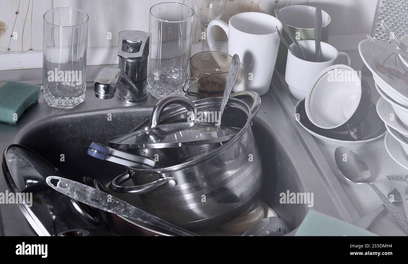A huge pile of unwashed dishes in the kitchen sink and on the ...