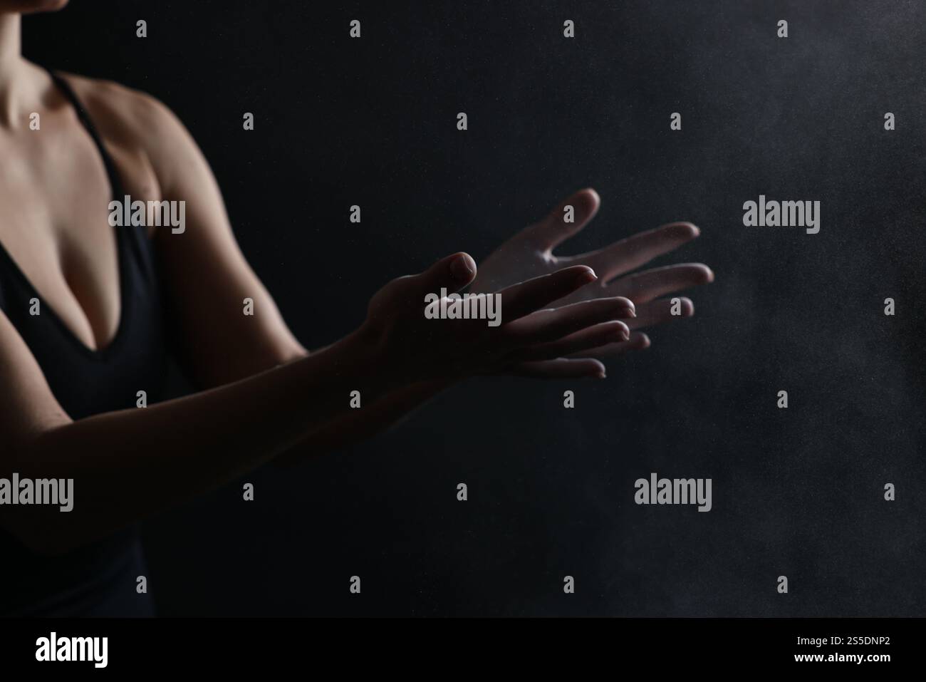 Woman clapping hands with talcum powder before training on black ...