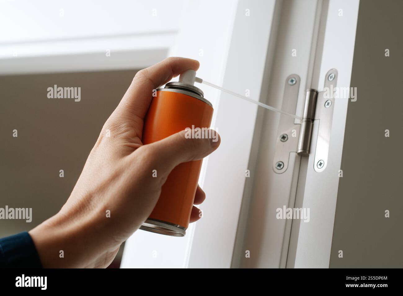 closeup of a man spraying some lubricating oil on the hinge of a white ...