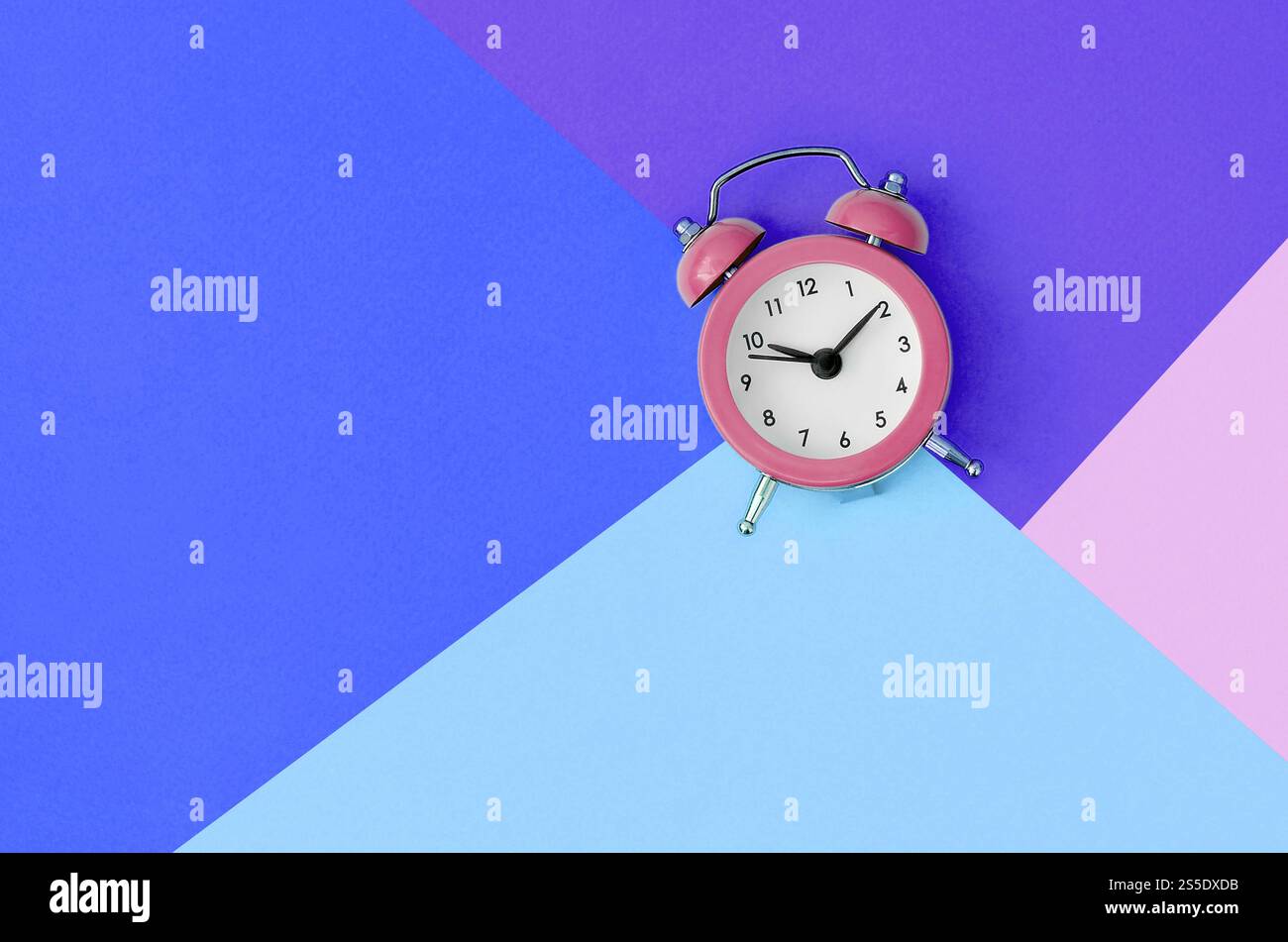 A small pink alarm clock is located between areas of blue, violet and ...