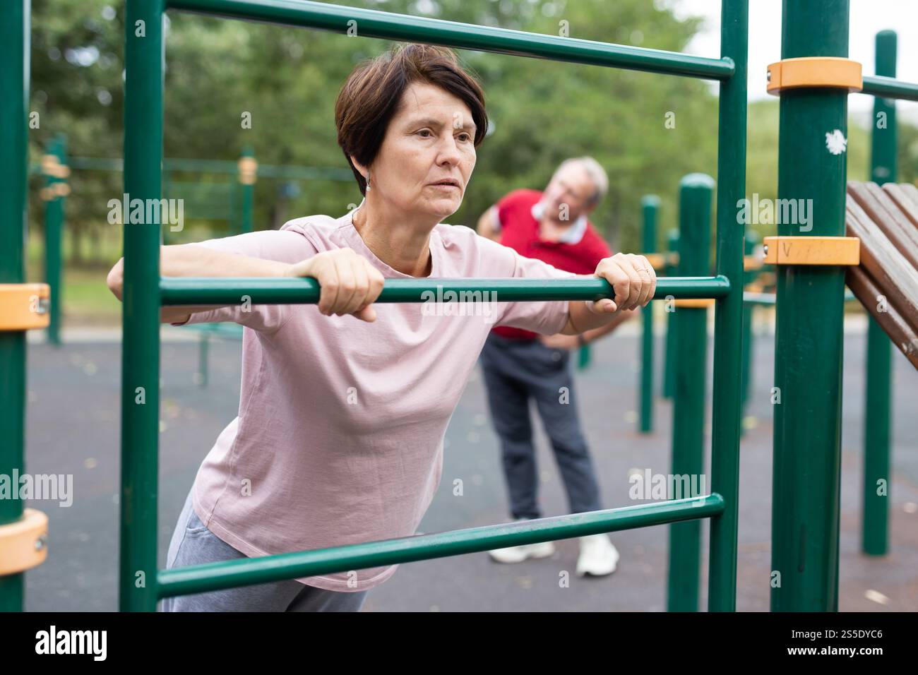 Mature woman doing push-ups from the crossbar on outdoor sports ground ...