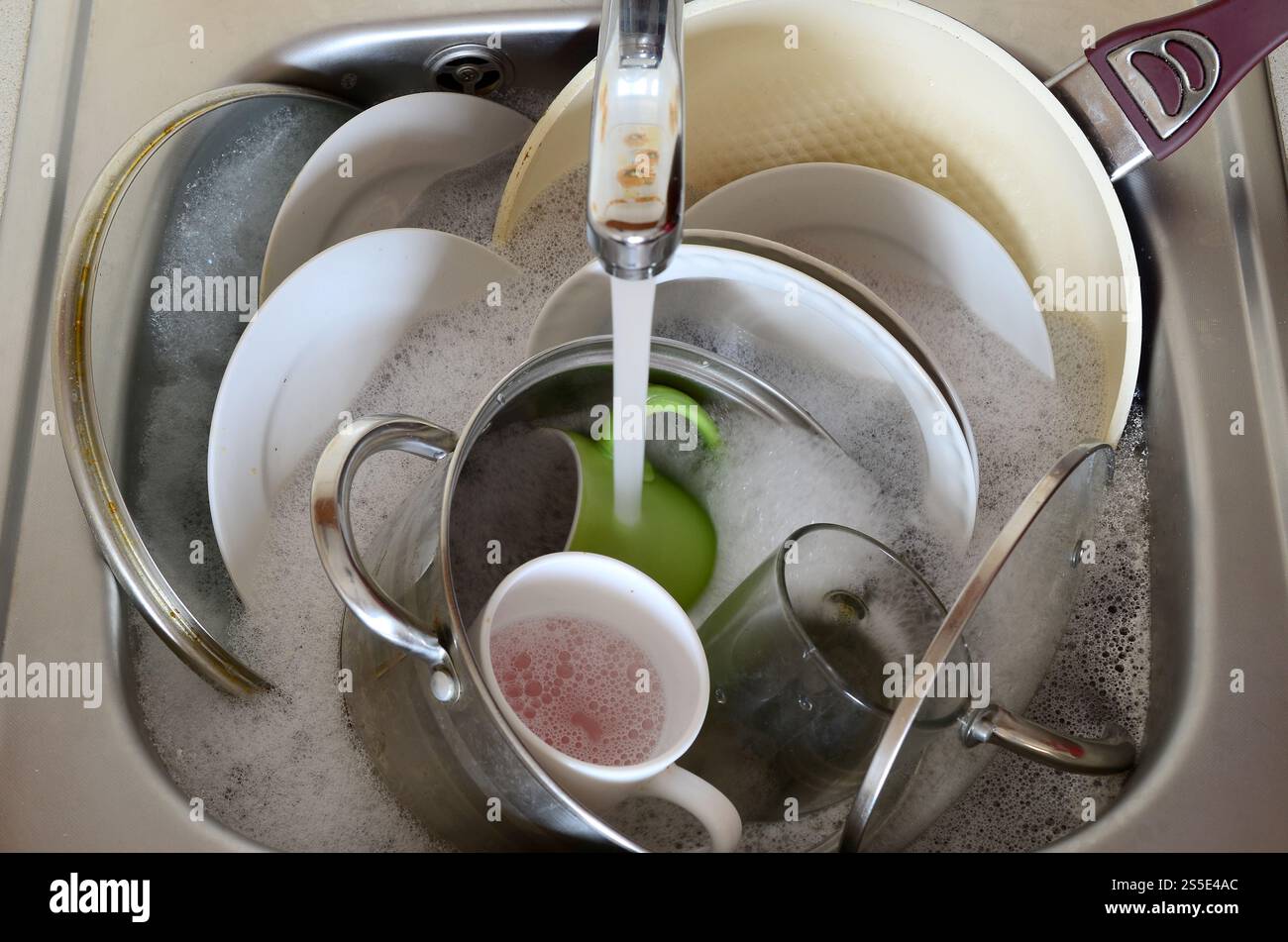 Dirty dishes and unwashed kitchen appliances lie in foam water under a ...