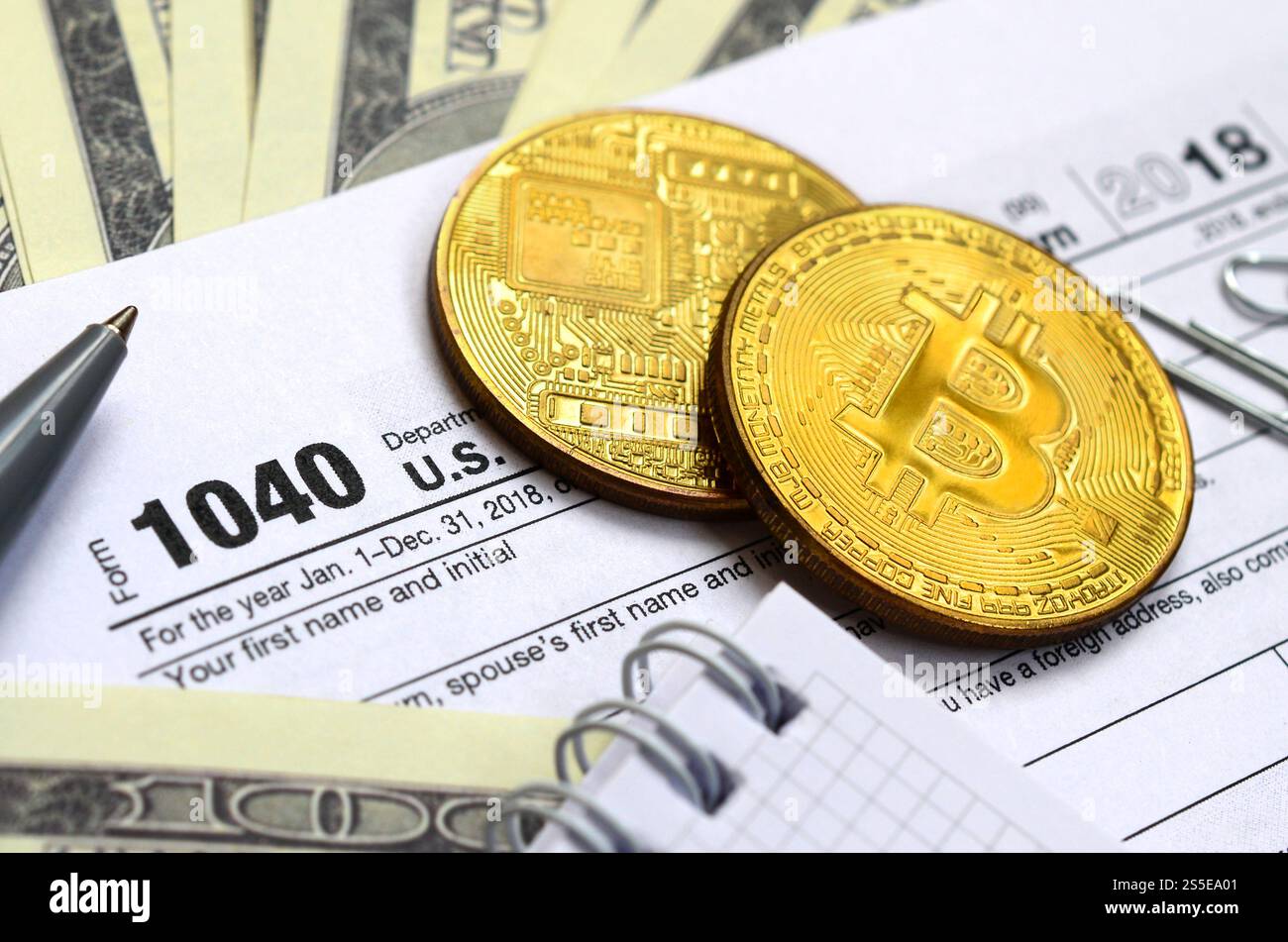 The pen, bitcoins and dollar bills is lies on the tax form 1040 U.S ...