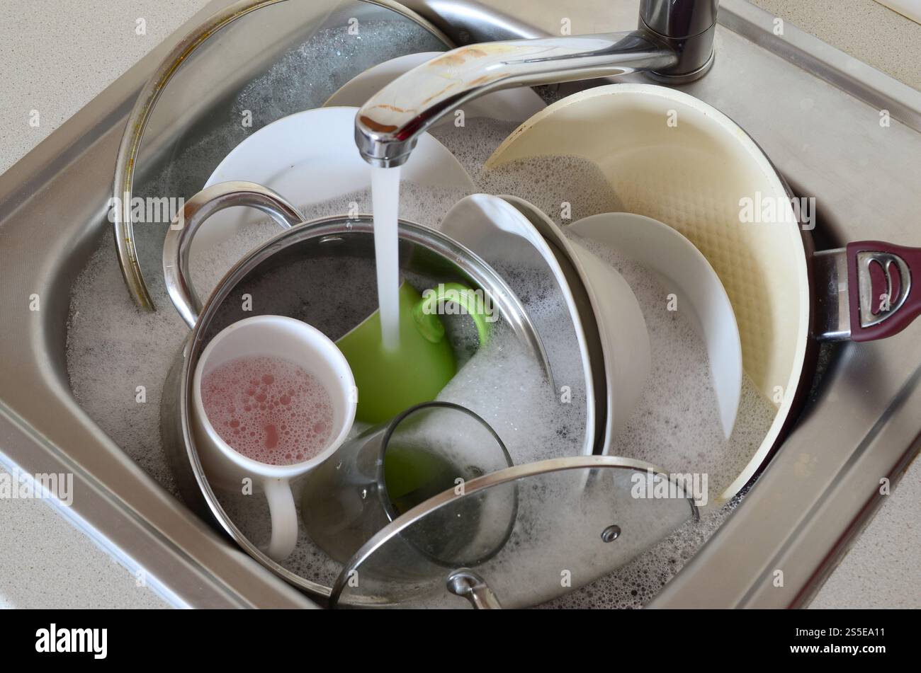 Dirty dishes and unwashed kitchen appliances lie in foam water under a ...