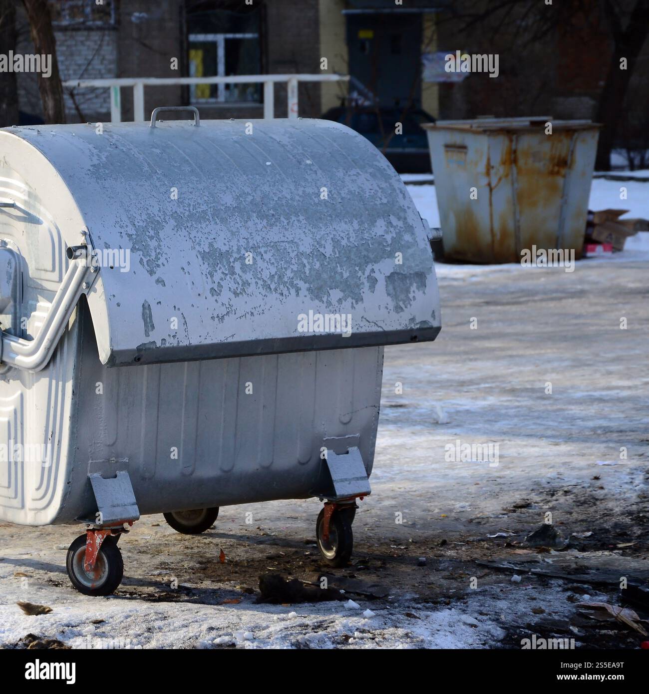 A silver garbage container stands near residential buildings in winter ...