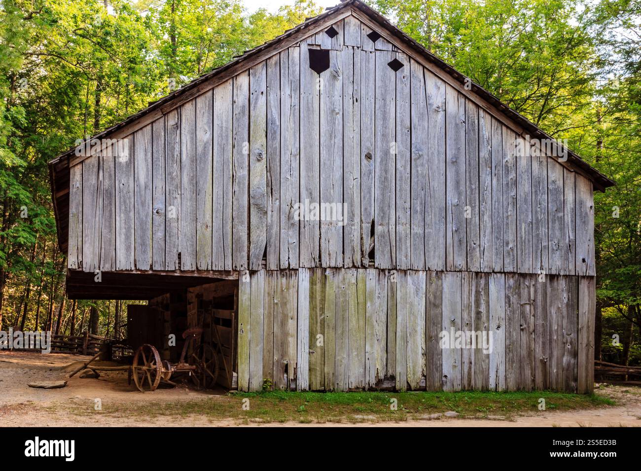 A large, old barn with a wheelbarrow in front of it. The barn is made ...