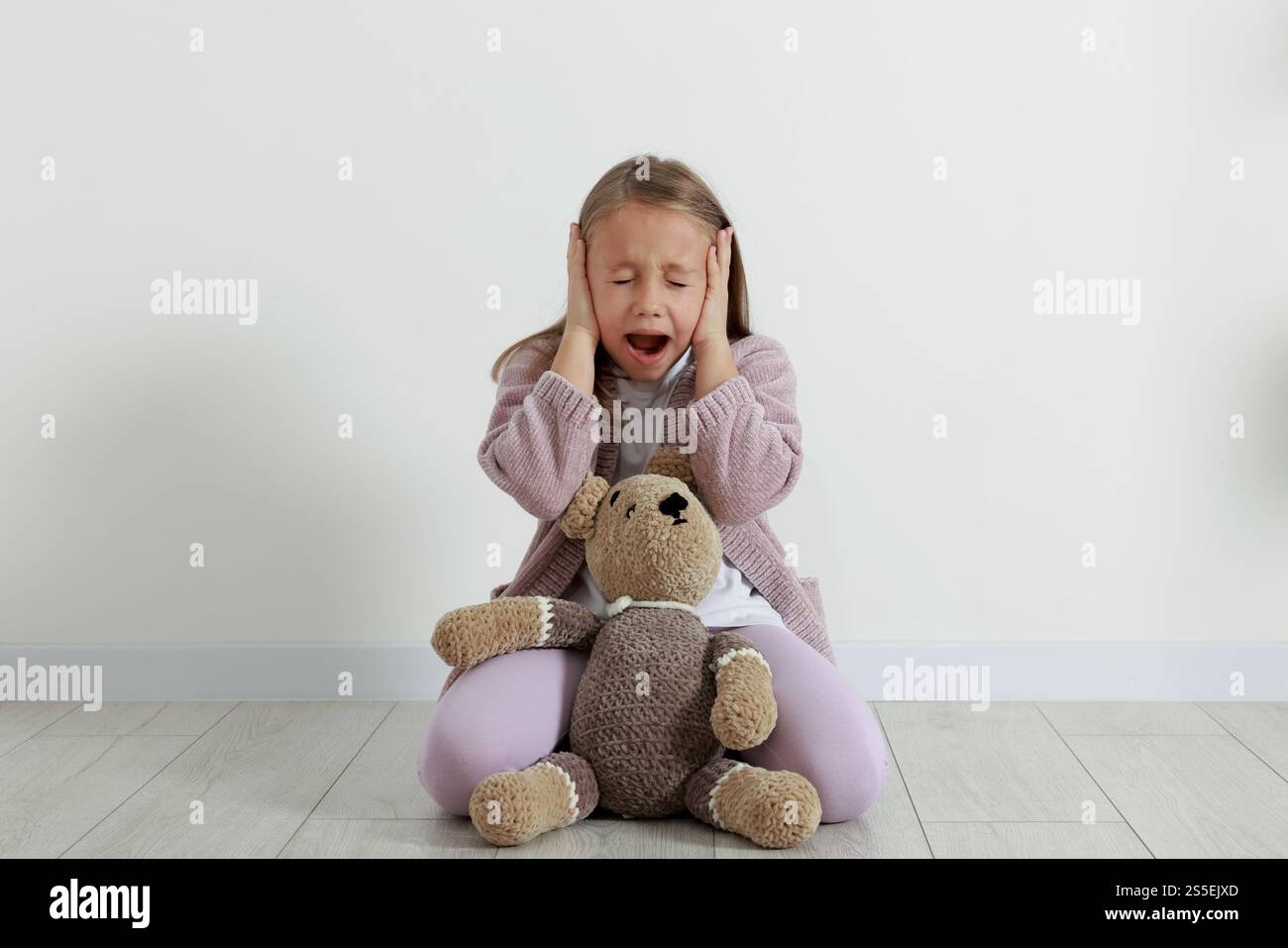 Autism concept. Scared little girl covering her ears on floor at home ...