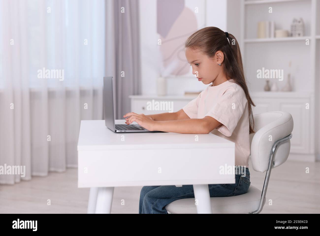 Girl with correct posture using laptop at white desk indoors Stock ...