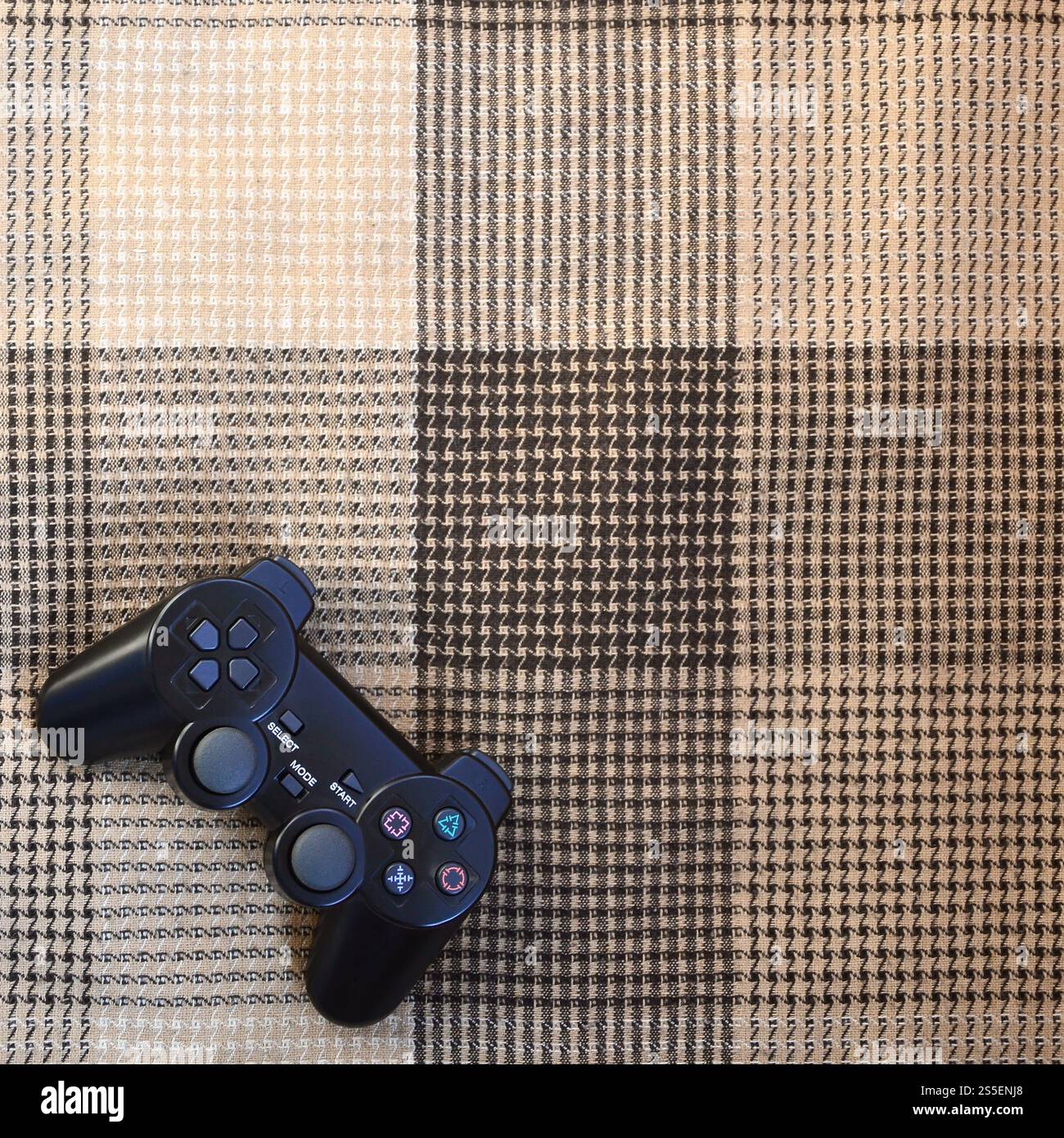 Modern black video game controller lies on a checkered beige and black ...