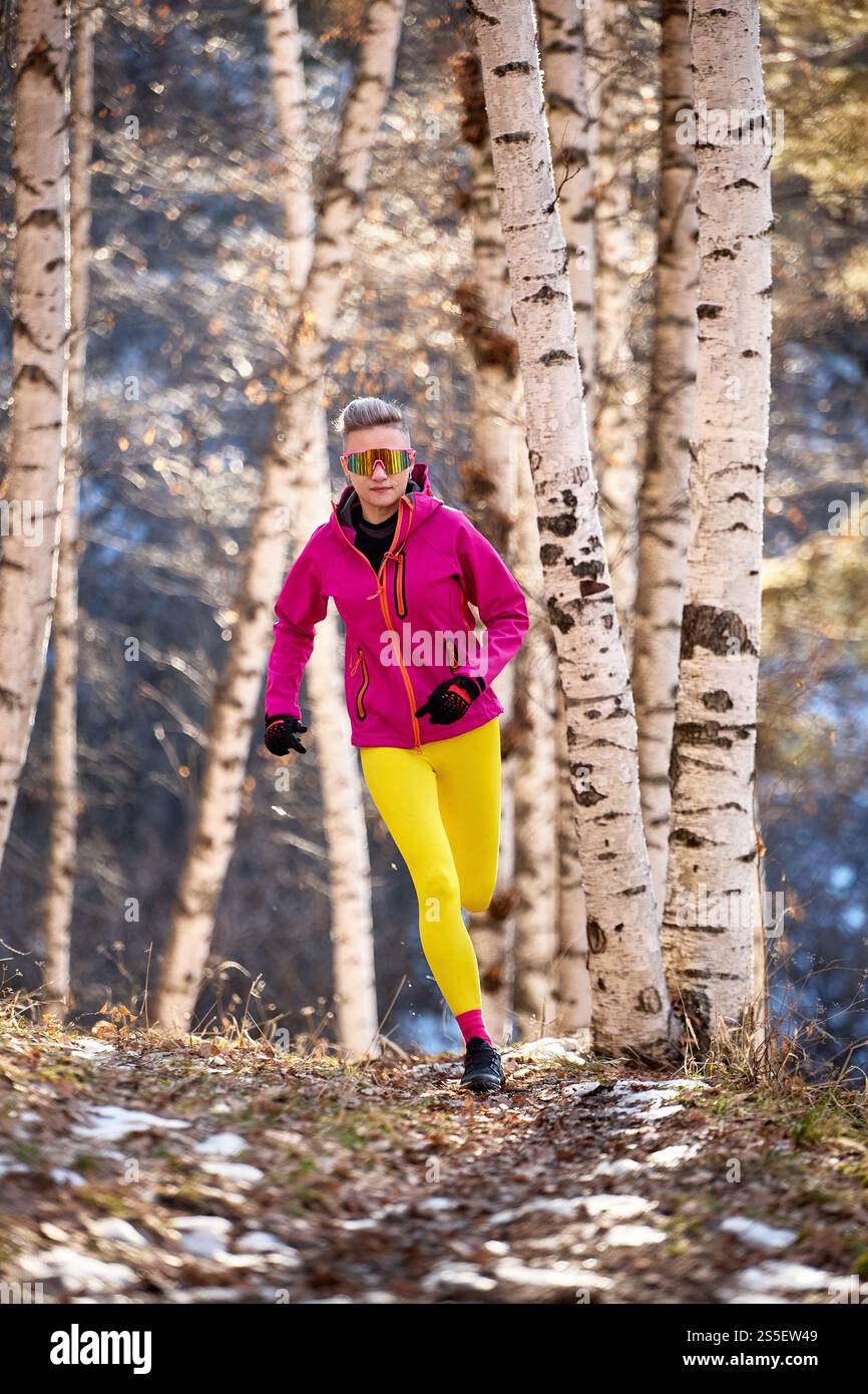 Athletic runner woman in pink jacket and yellow jogging pants running ...