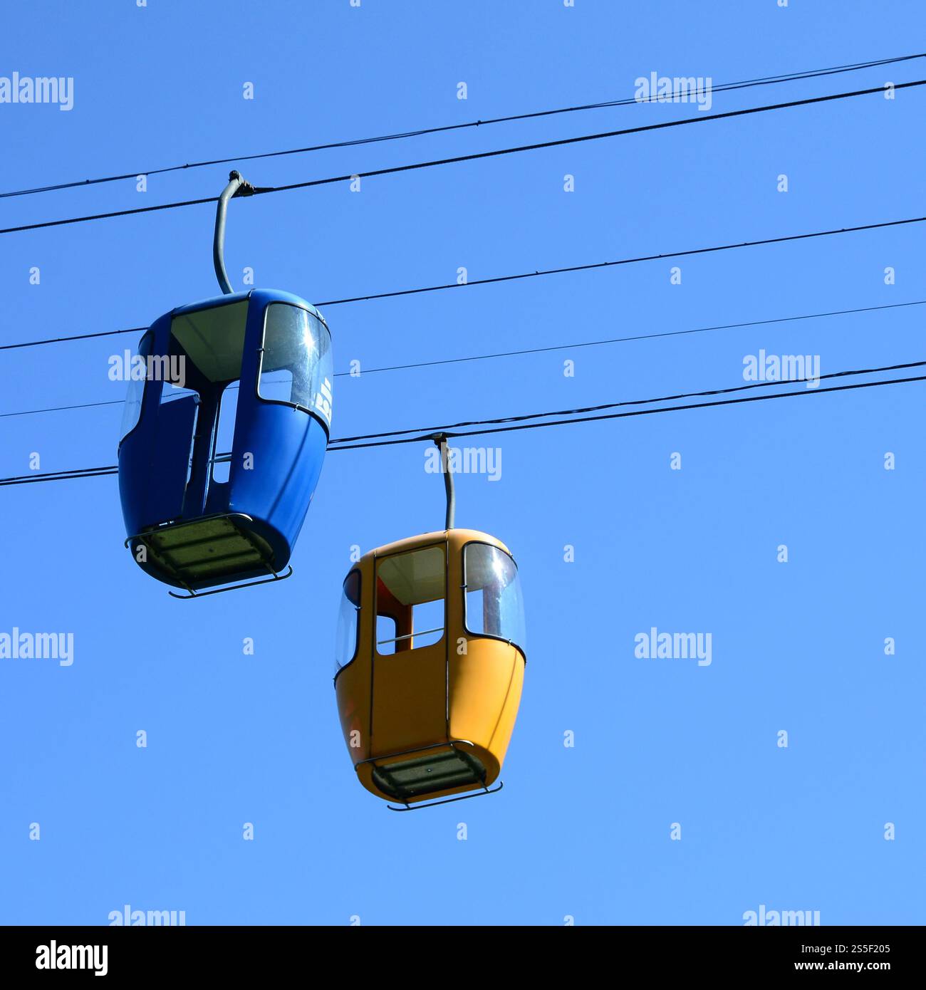 Blue and yellow passenger cable way cabins in the clear blue sky. Blue ...