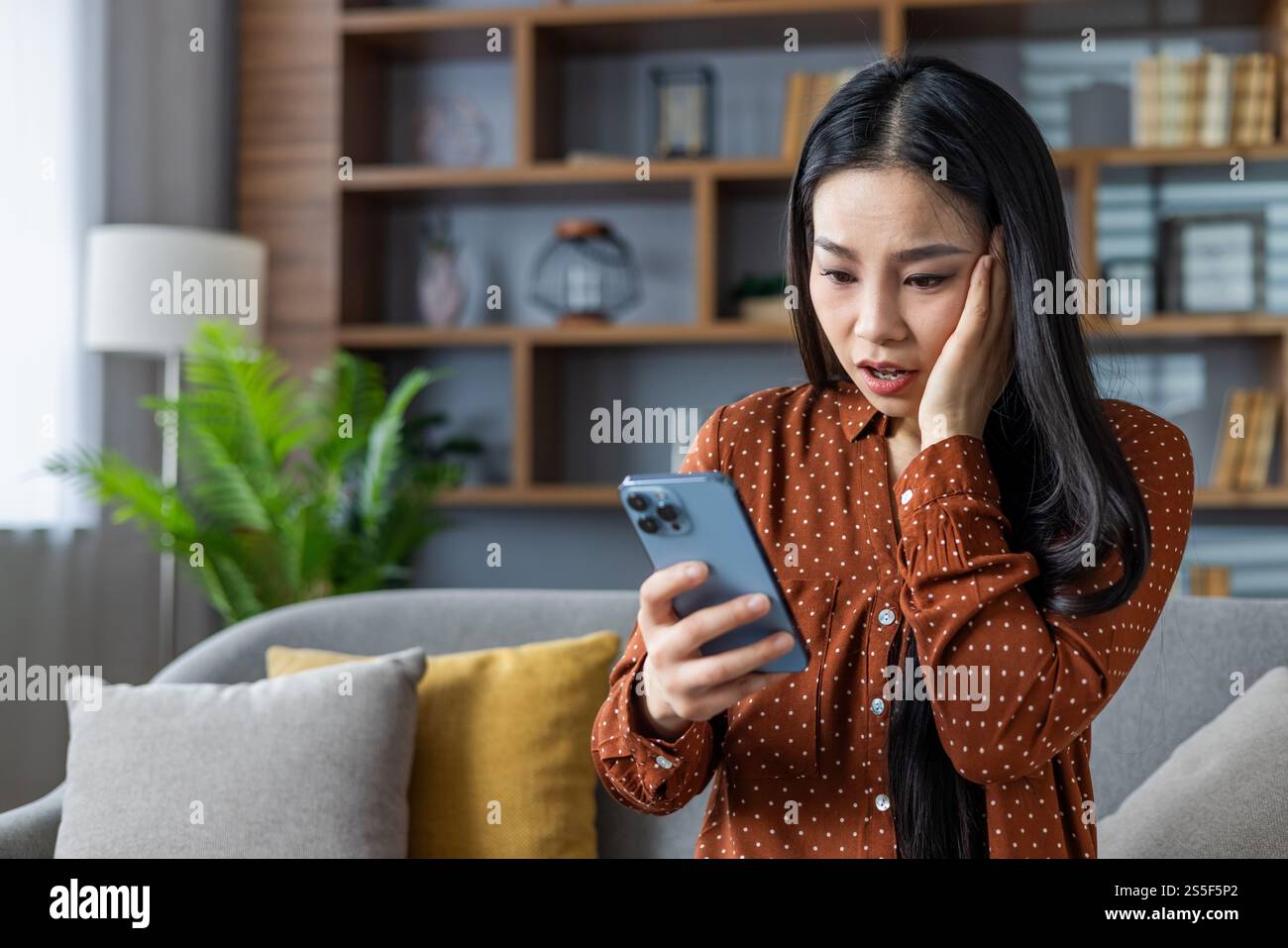 Asian woman experiencing shock while reading phone message in home ...