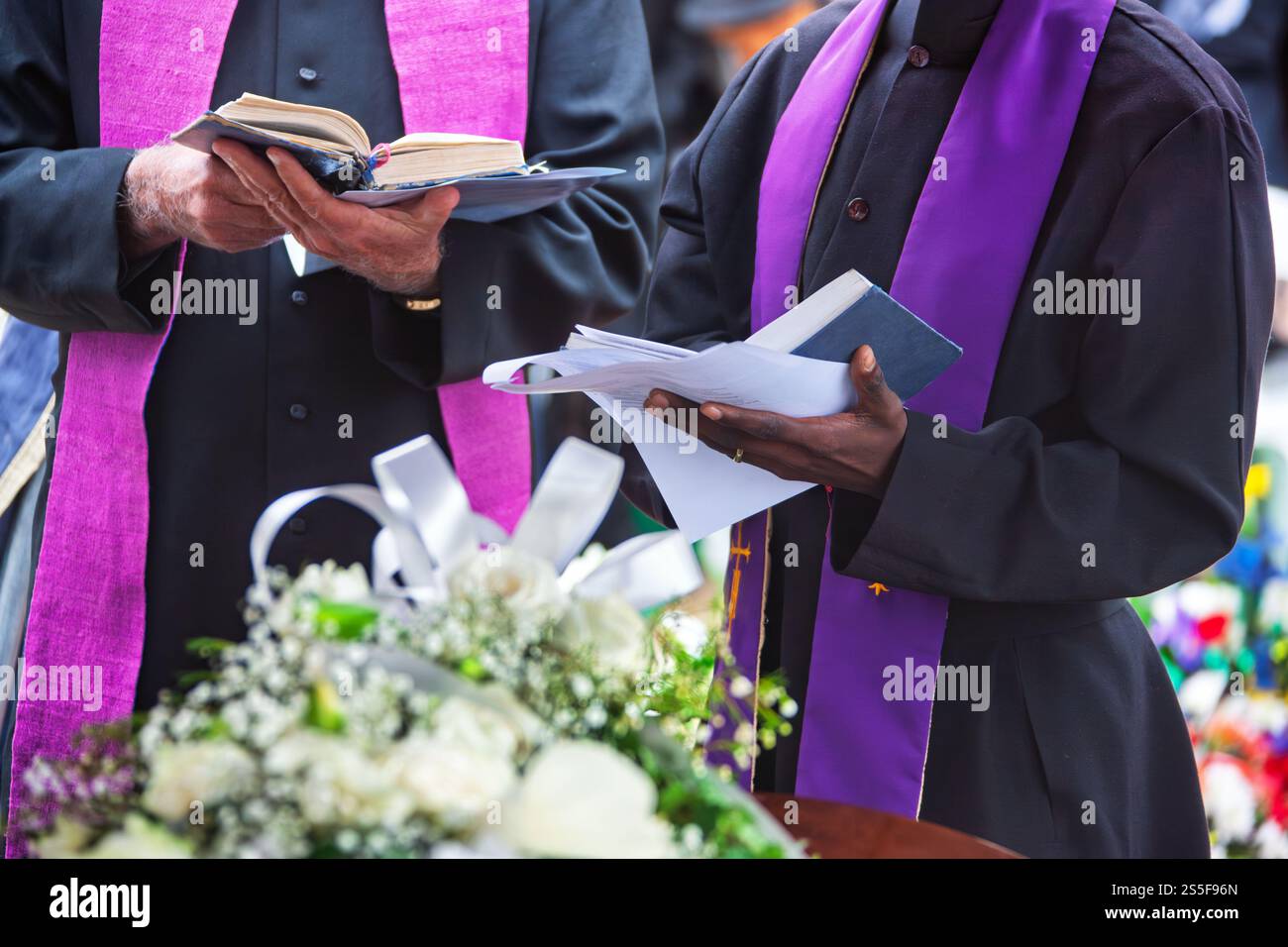 two priests reading prayers at a funeral to bless the grave at the ...