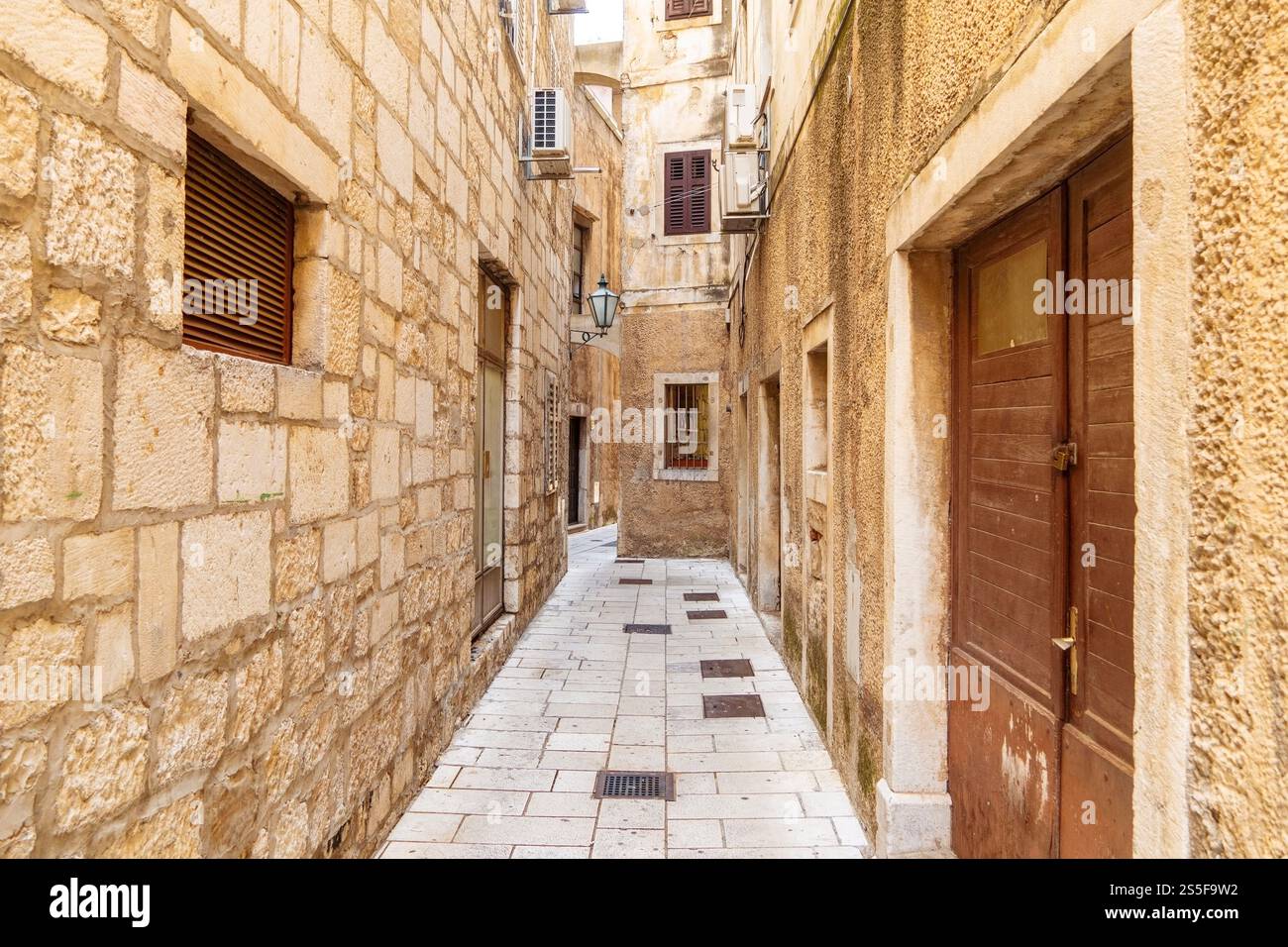 Narrow cobblestone street lined with old stone buildings under a bright ...