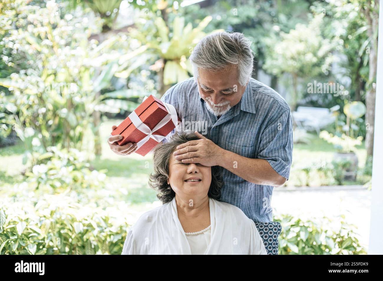 Smiling senior husband making surprise giving gift box to his wife ...