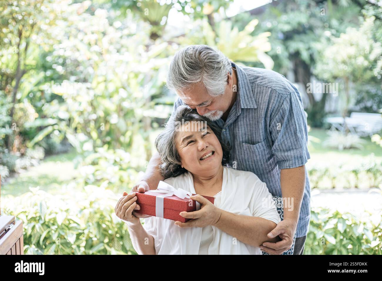 Smiling senior husband making surprise giving gift box to his wife ...