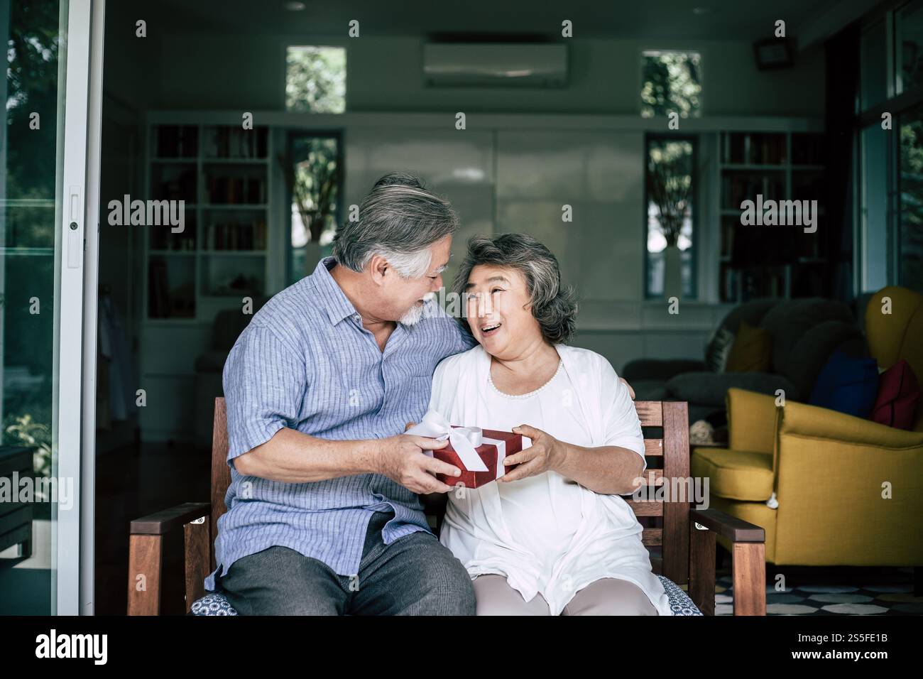 Smiling senior husband making surprise giving gift box to his wife ...