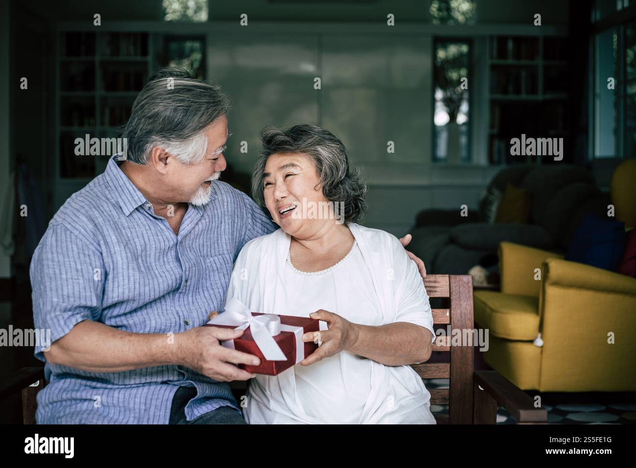 Smiling senior husband making surprise giving gift box to his wife ...