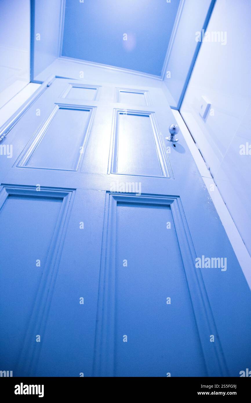 Blue-tinted image of a closed wooden door with a metal doorknob, angled ...
