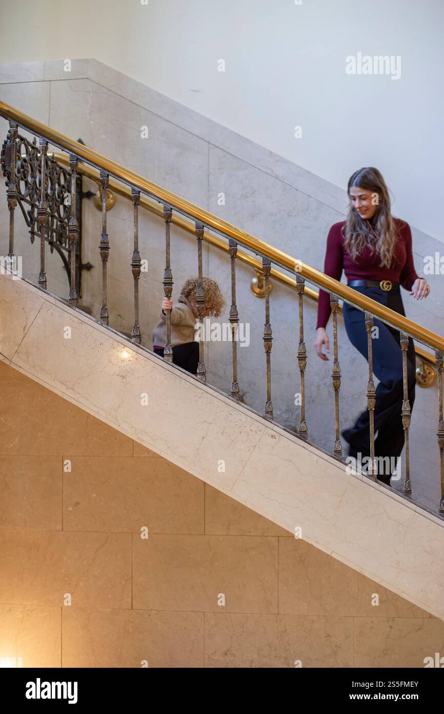 Woman and child descending a grand staircase with ornate railing in an elegant building ...