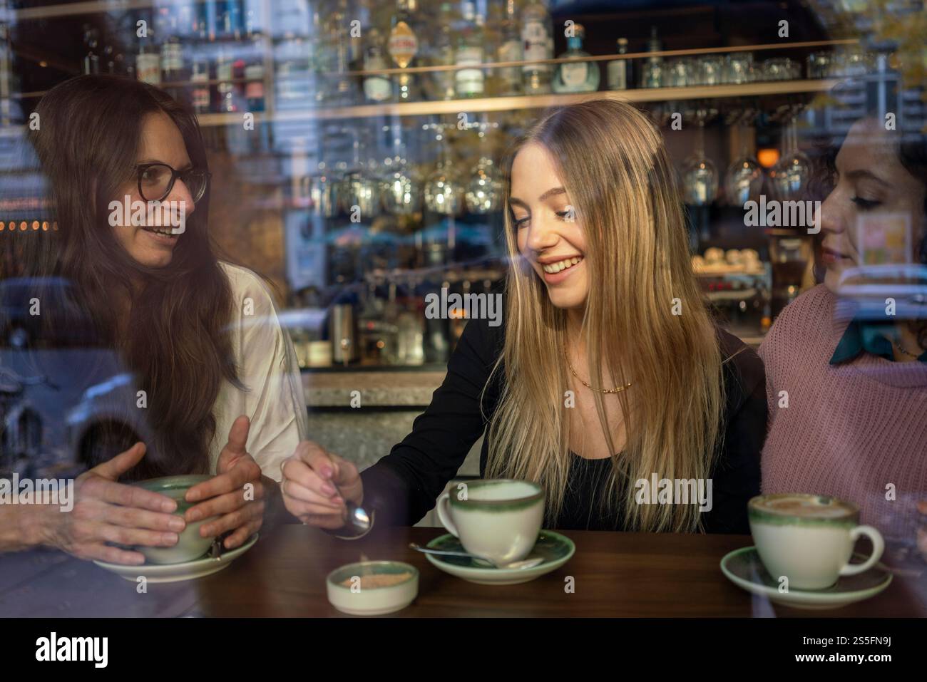 Three women enjoy conversation over coffee inside cozy cafe hi-res ...