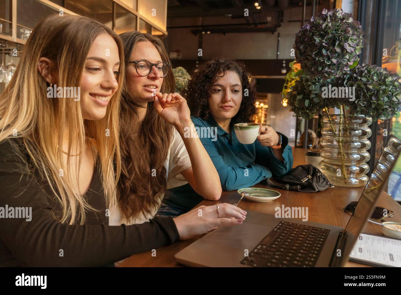 Three women engaging conversation cafe table while one operates laptop ...
