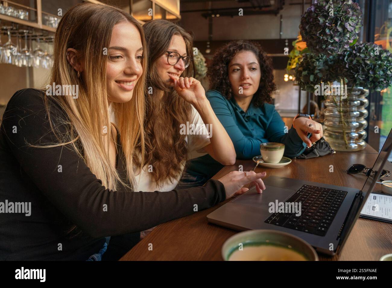 Three women using laptop enjoying coffee cafe table hi-res stock ...