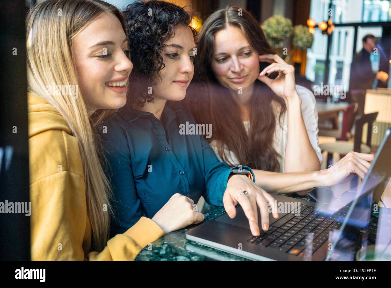 Three women smiling looking laptop screen together indoor setting hi ...