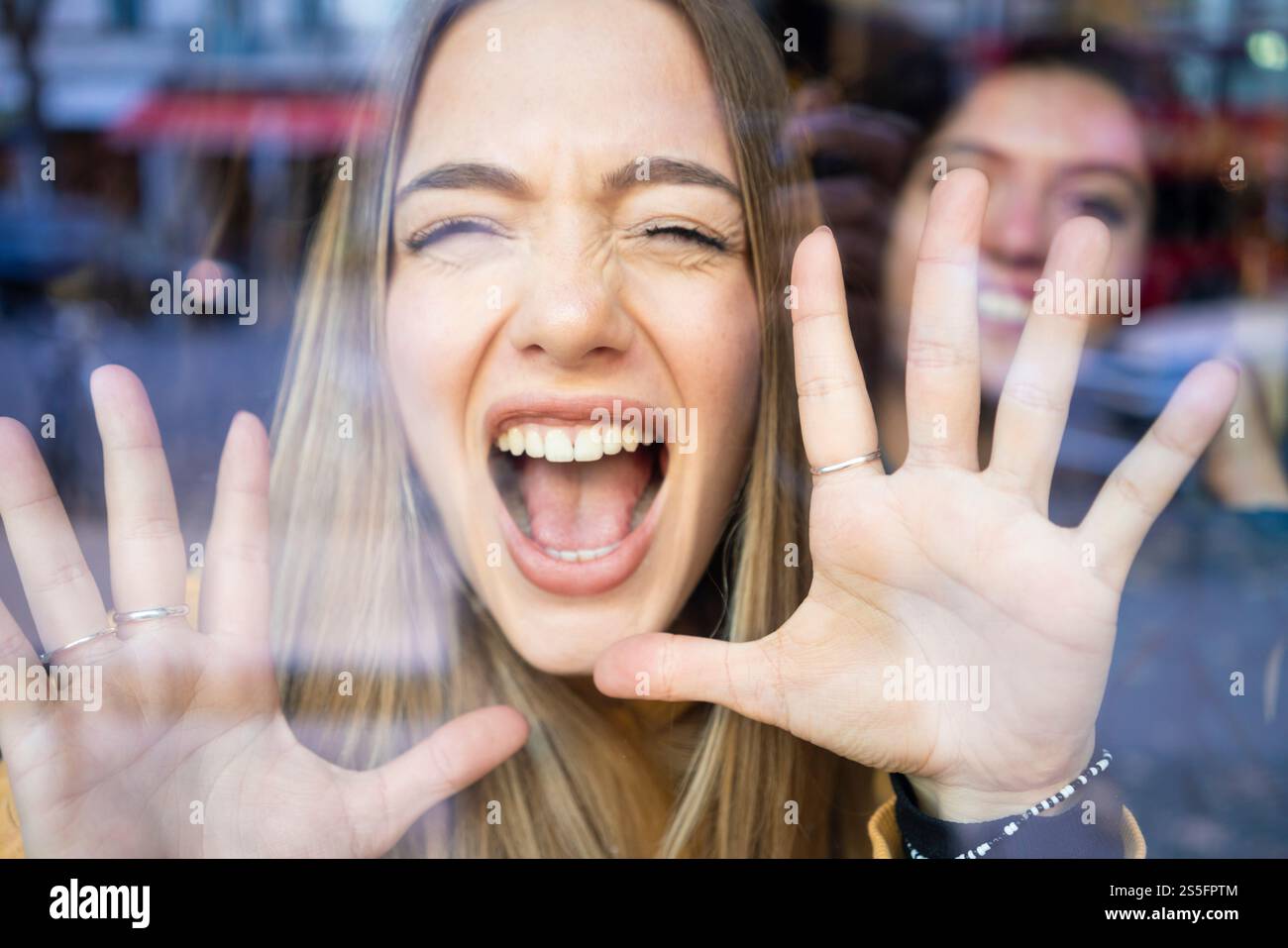 Joyful young woman pressing her hands against a glass window with her eyes closed and mouth open ...