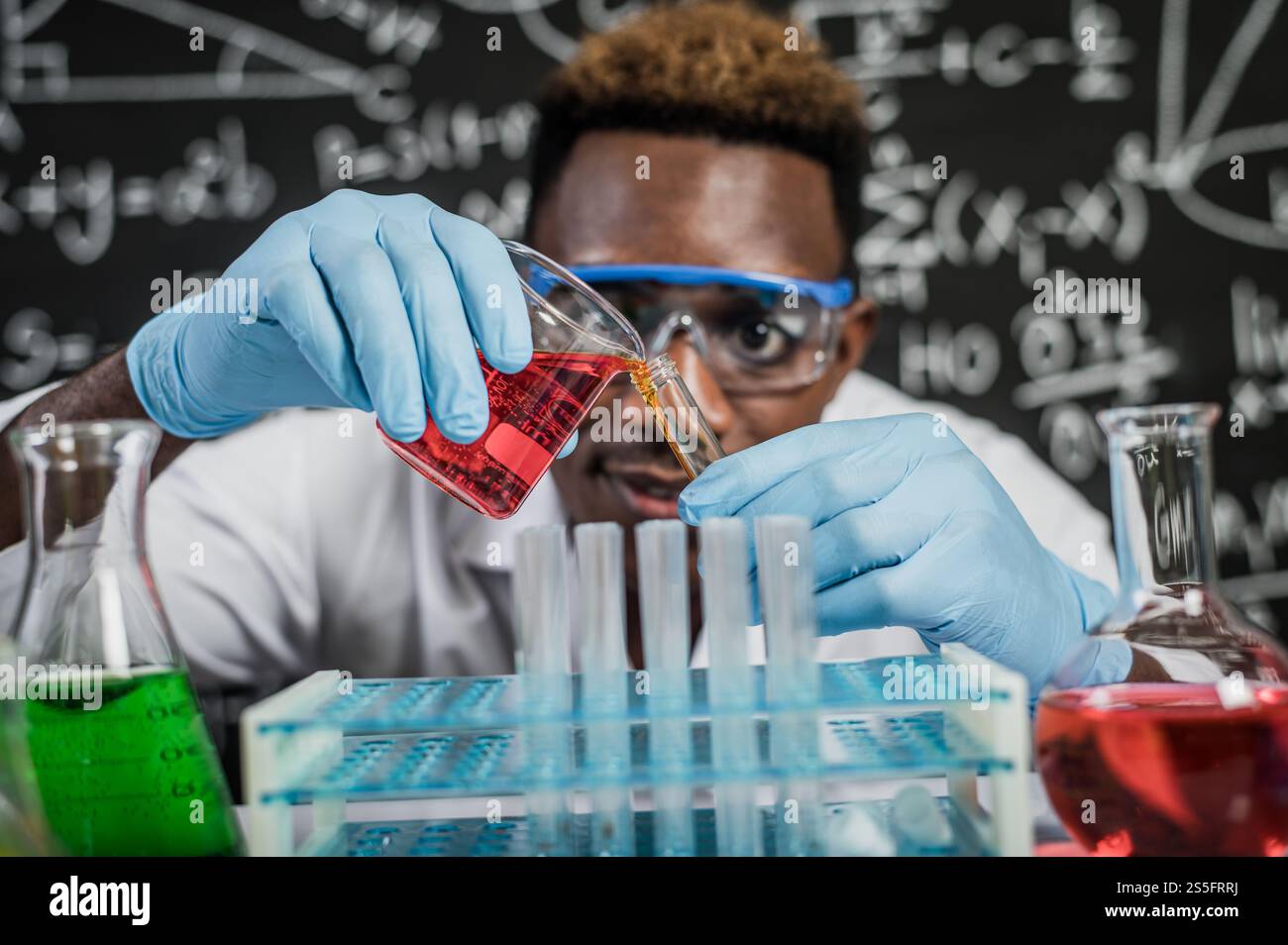 Scientists mix red and orange chemicals in a glass at the laboratory ...
