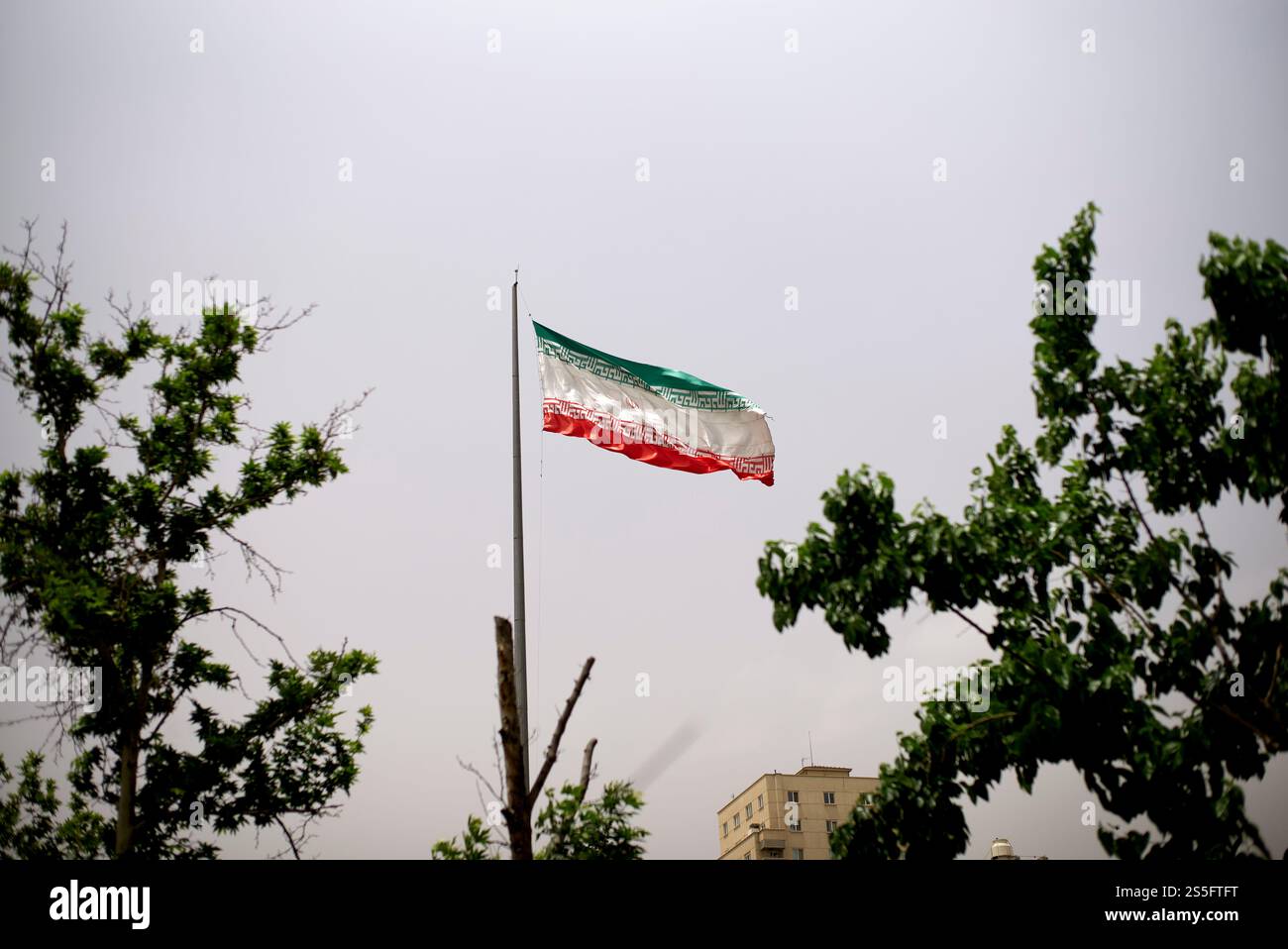 Iranian flag waving above a cityscape on an overcast day, Teheran, Iran ...