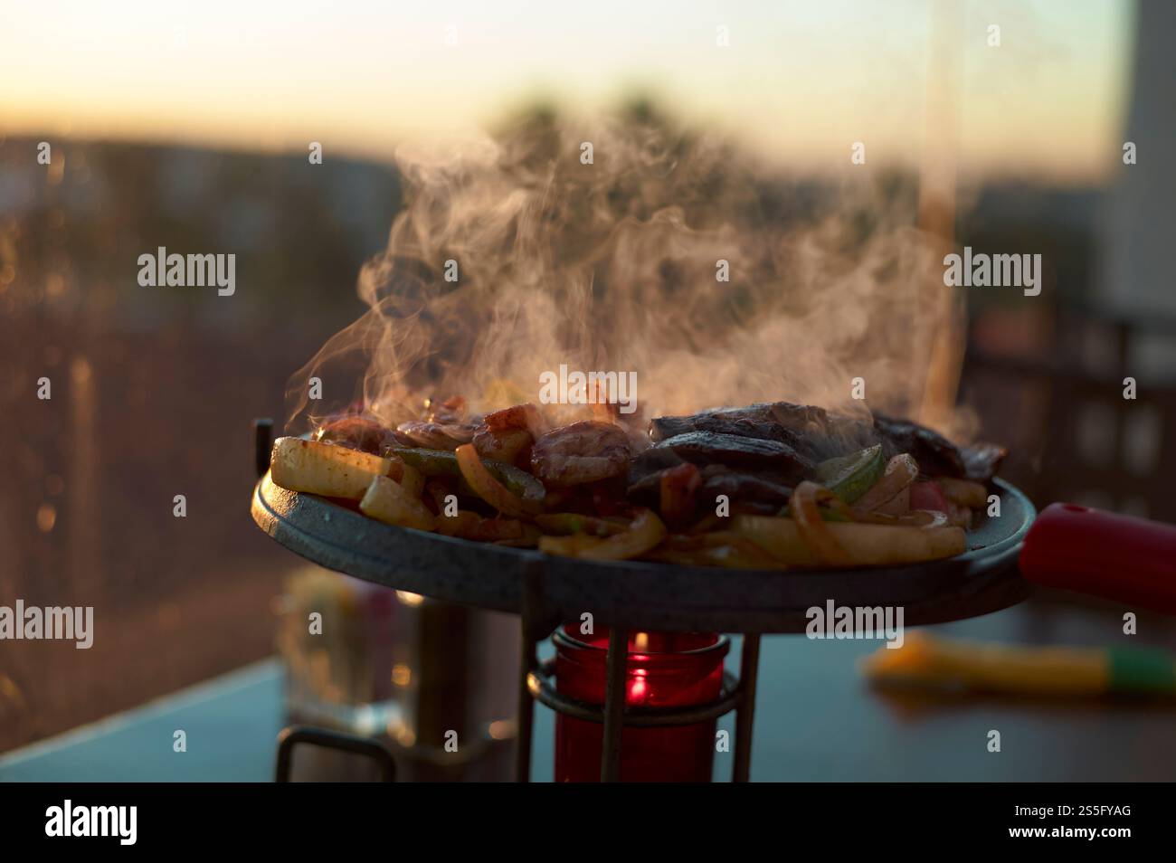 Sizzling barbecue grill with steaks and vegetables against a sunset ...