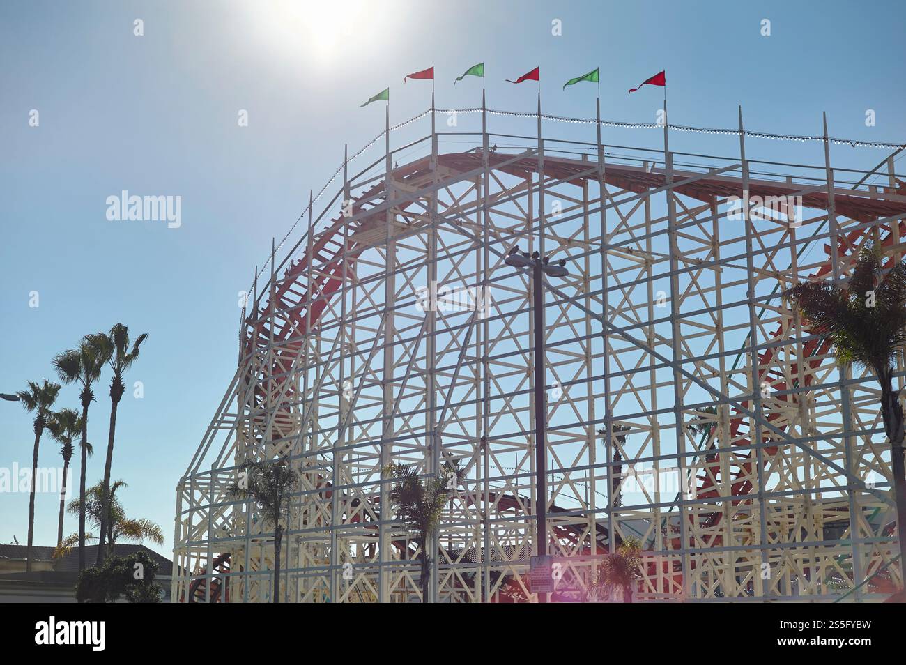 Sunlight gleams over a traditional wooden roller coaster flanked by ...