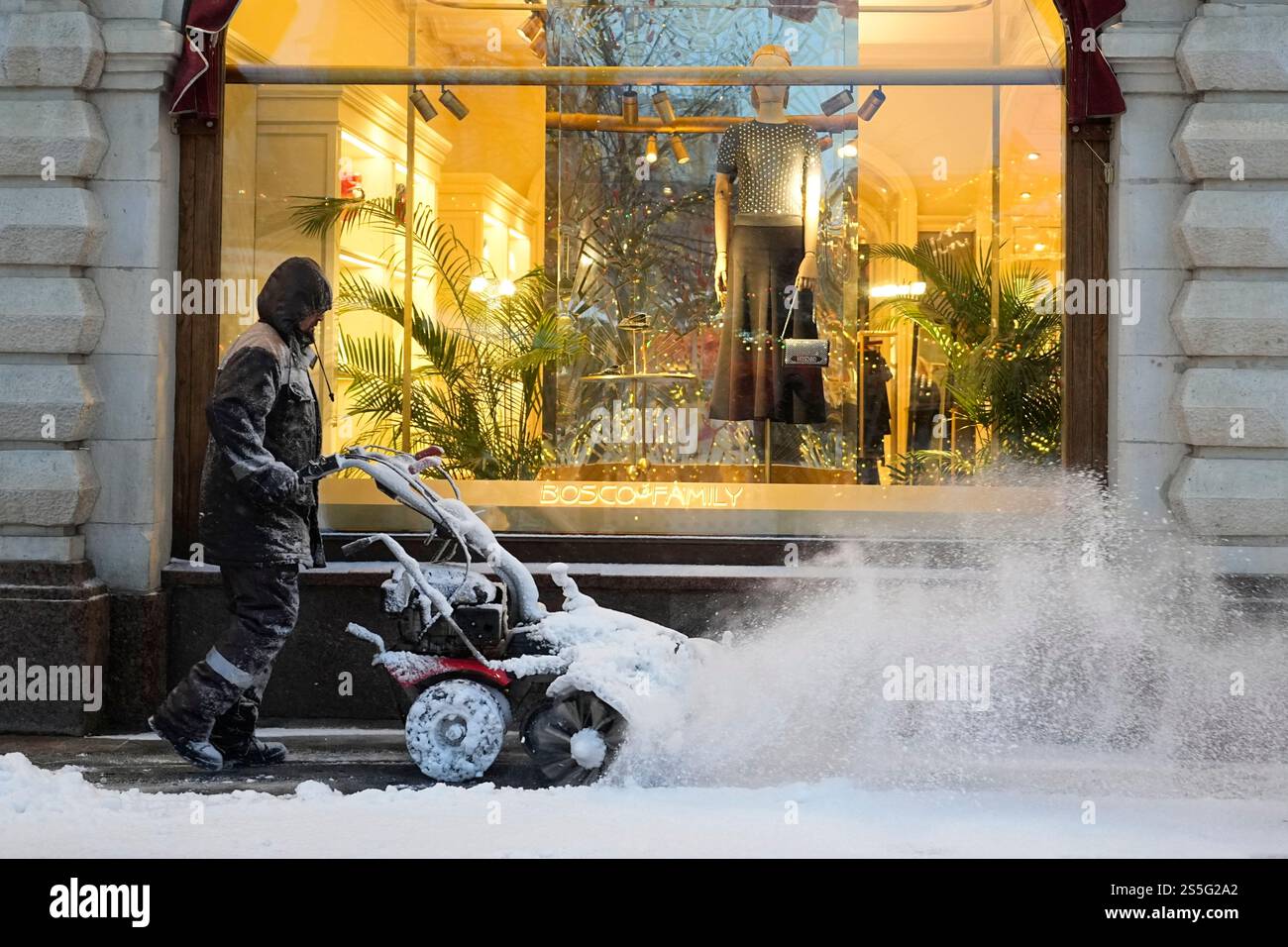 A man with a snowplough removes the snow next to a shopping window of ...