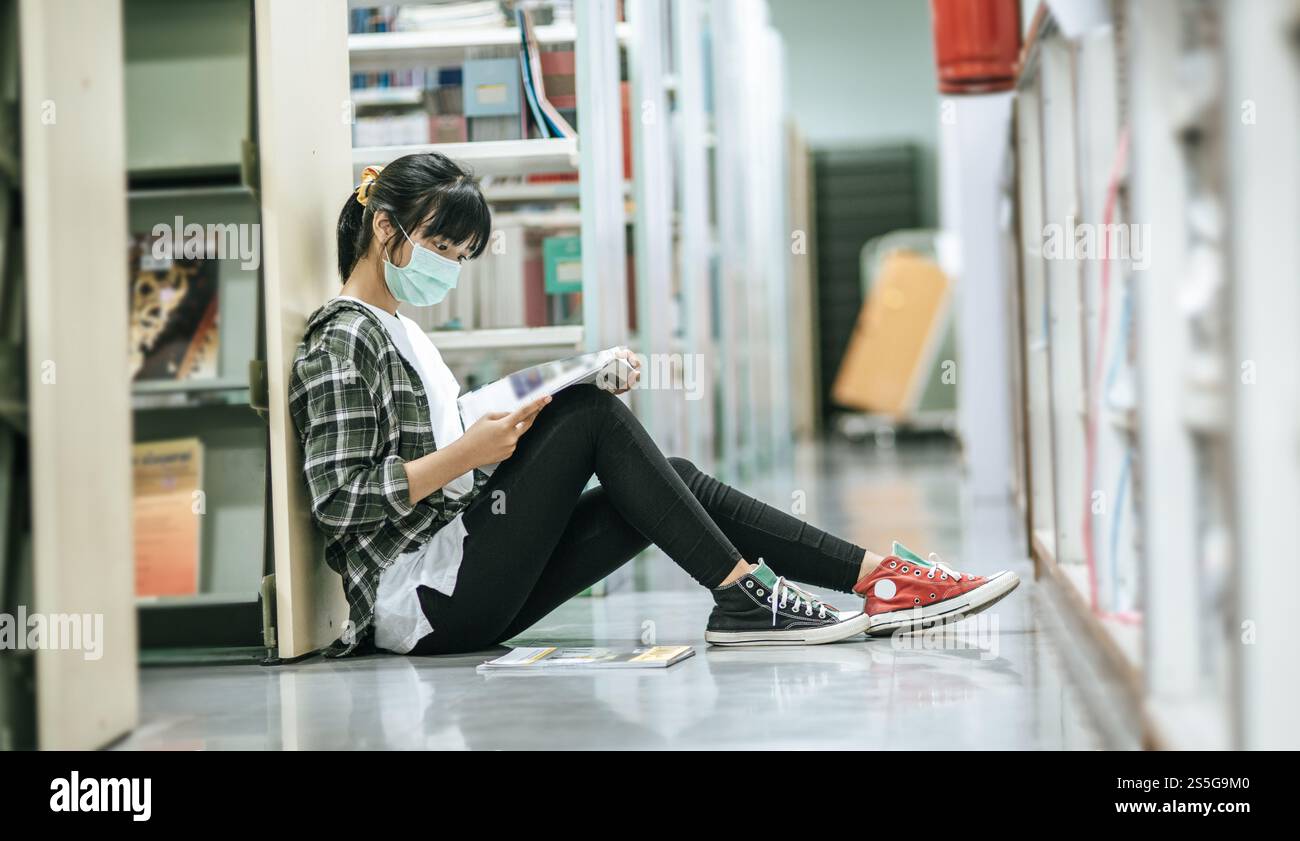 A woman wearing masks is sitting reading a book in the library Stock ...