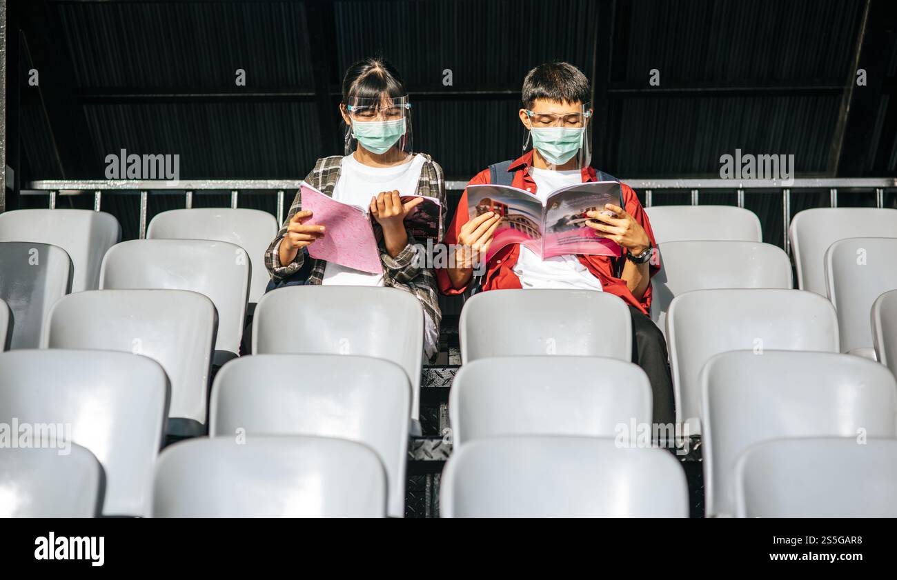 Male and female students wear masks and sit and read on the field chair ...