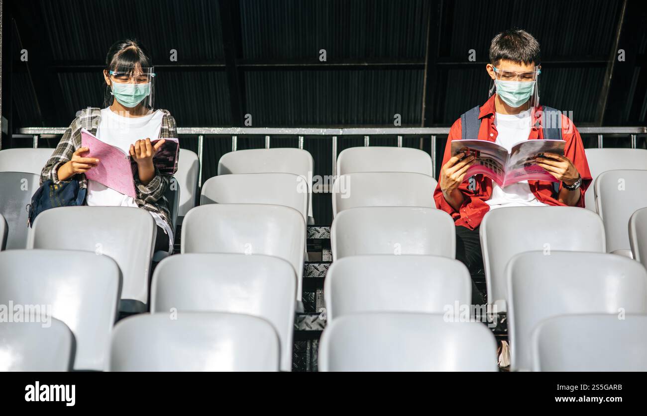 Male and female students wear masks and sit and read on the field chair ...