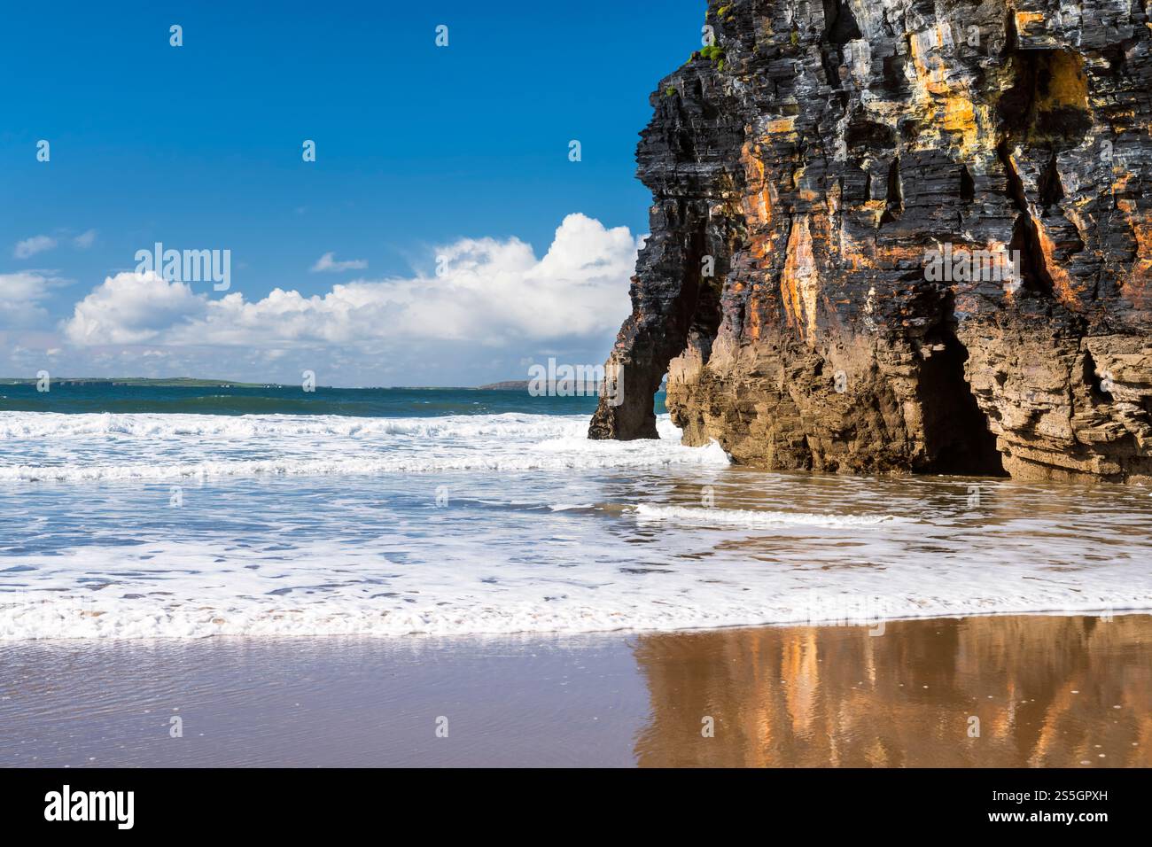 Ocean waves and picturesque cliff reflecting in wet sand at Ballybunion ...